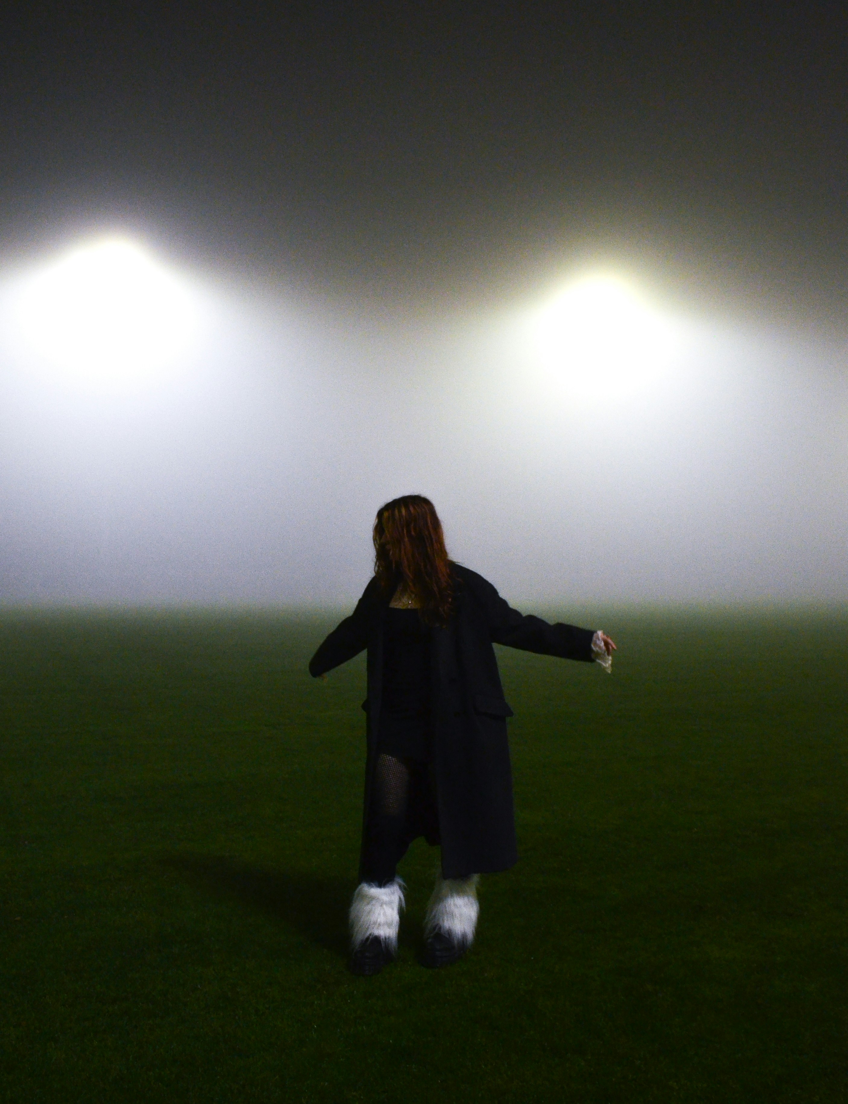 Midnight Vigil: A solitary figure in a foggy field under twin stadium lights