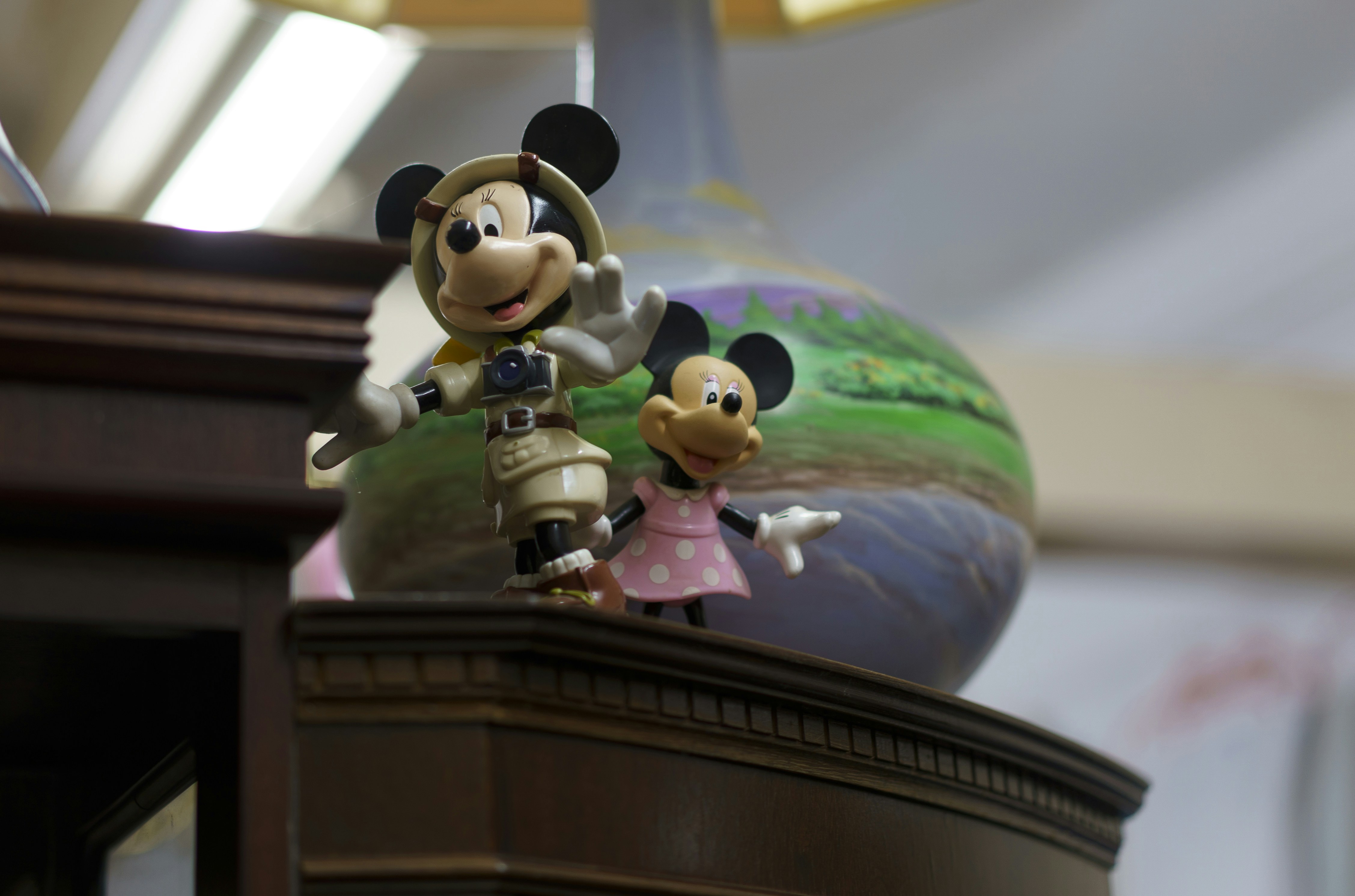Mickey and Minnie Mouse figurines on a wooden shelf in front of a lamp