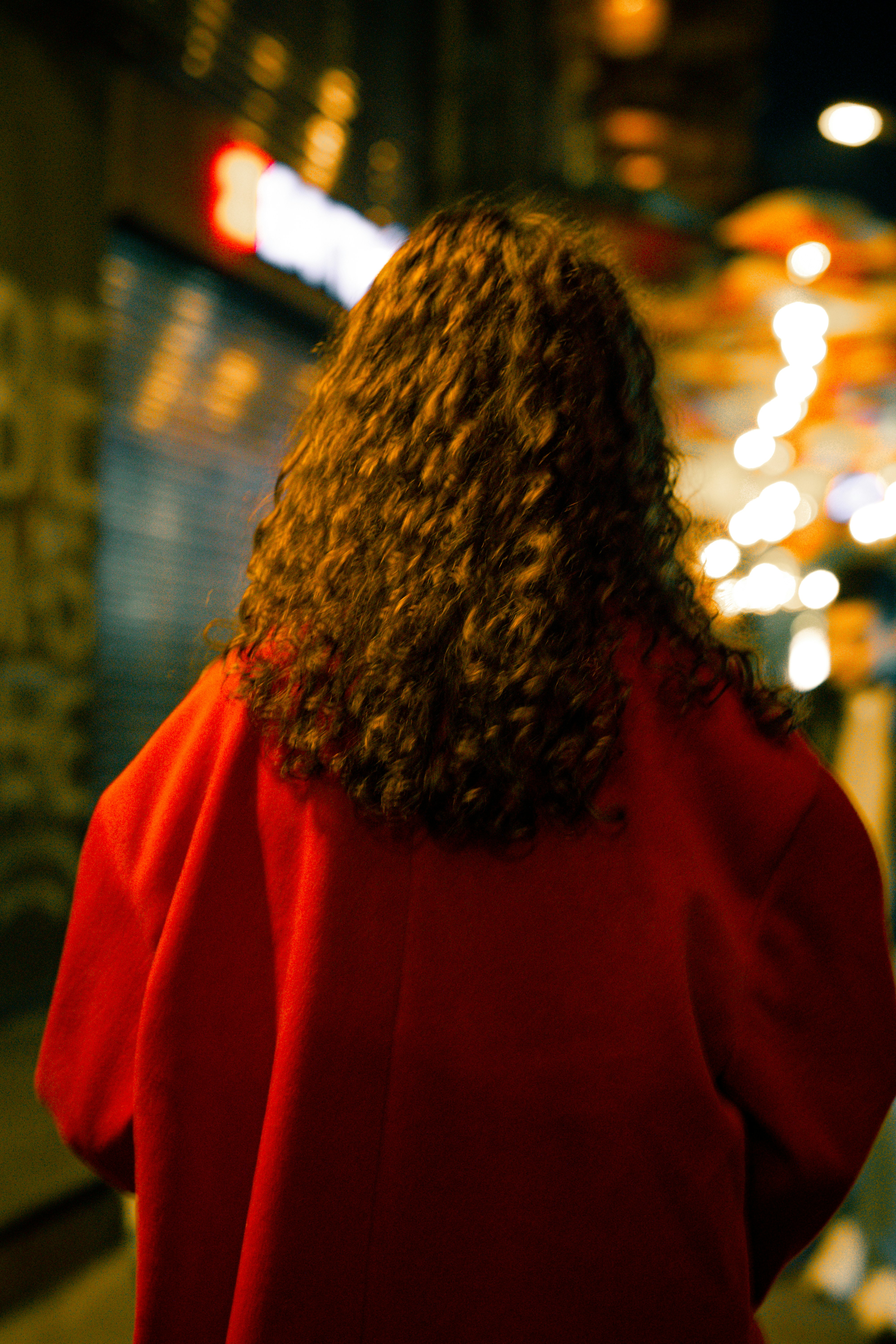 Emerging from the City Glow: Back of a Red-Cloaked Figure in Neon Night
