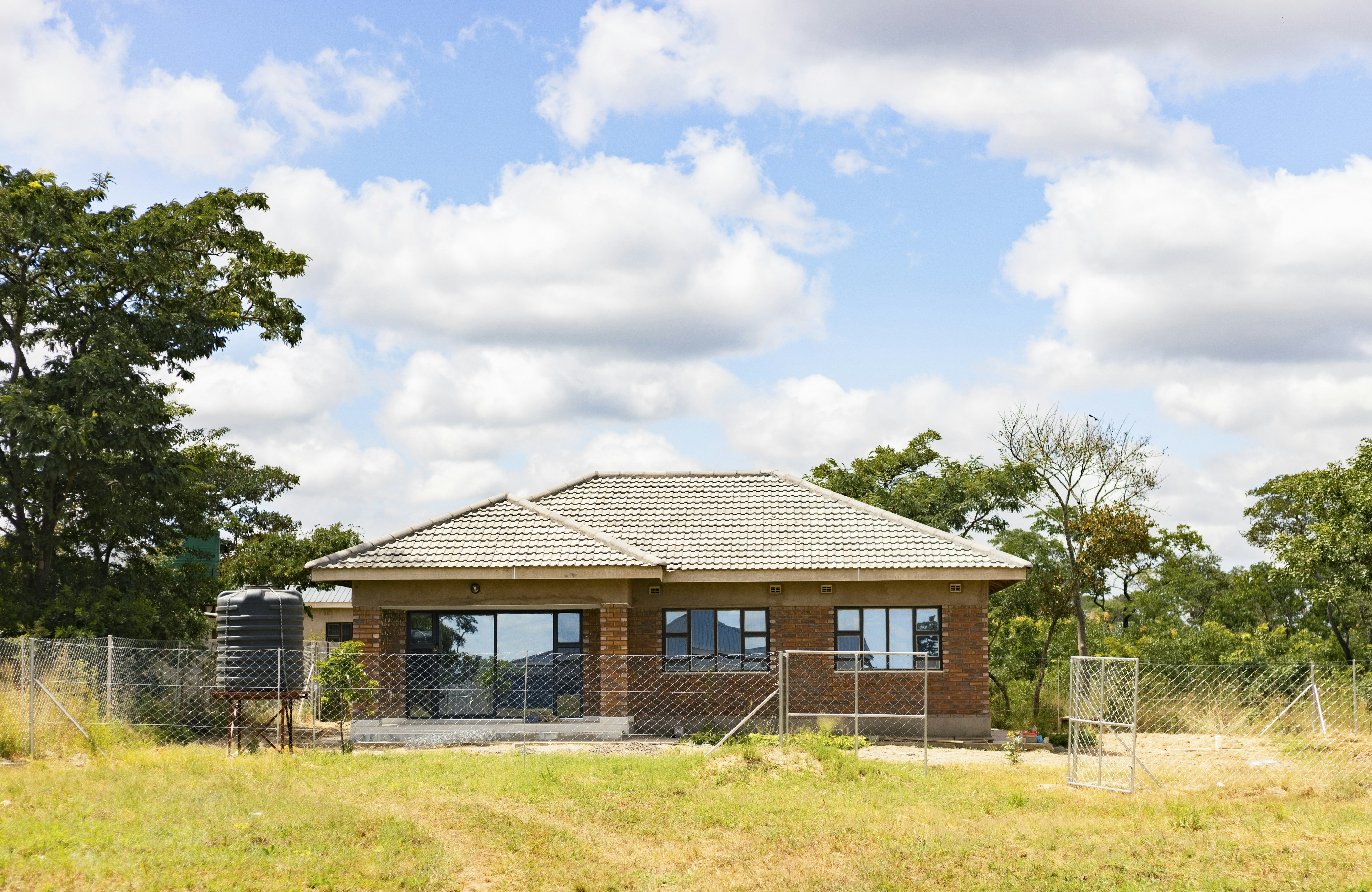 Brick House with Chain-Link Fence in Sunlit Clearing