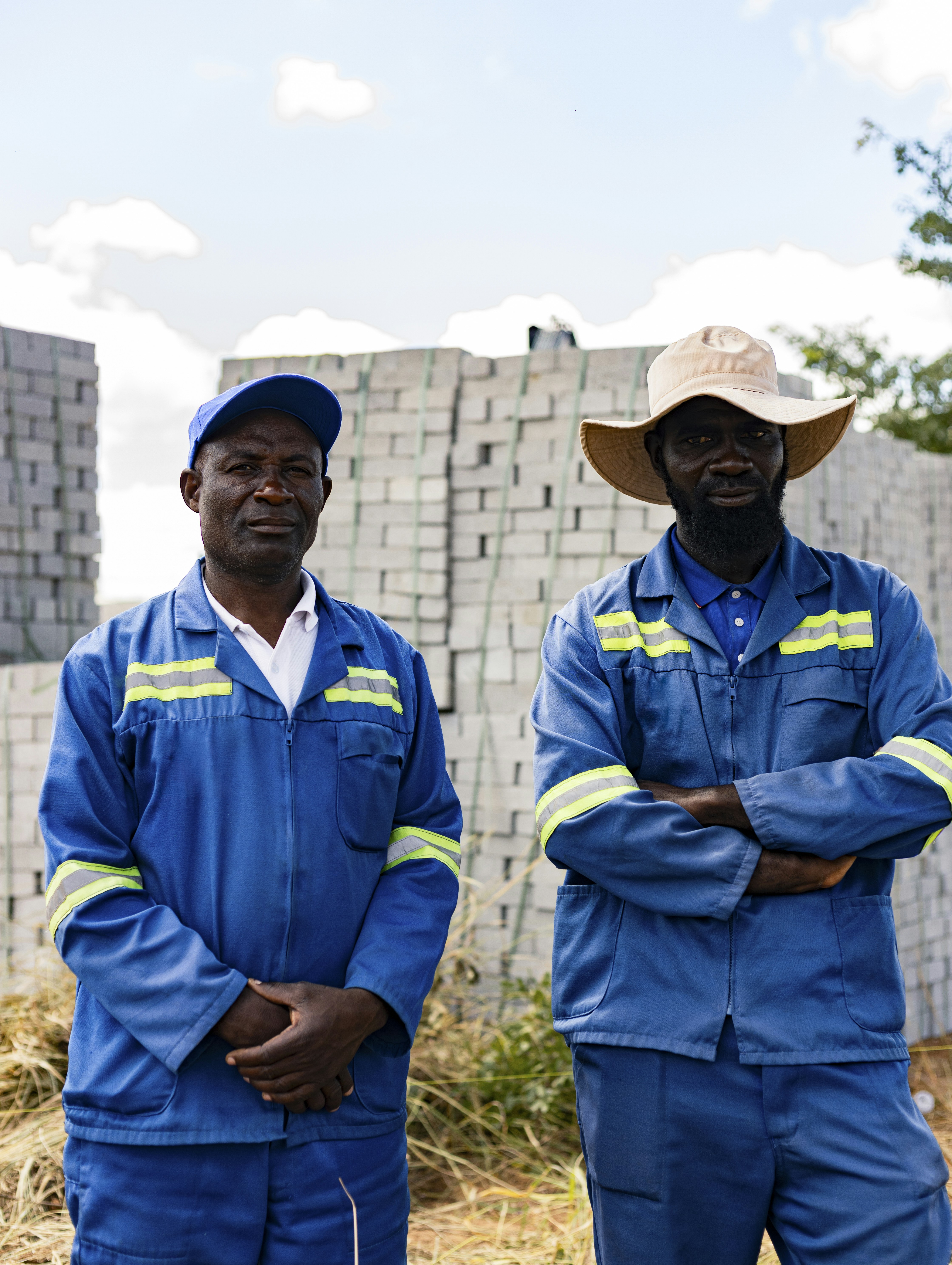 Blue-Covered Workers Standing in Front of Brick Stack