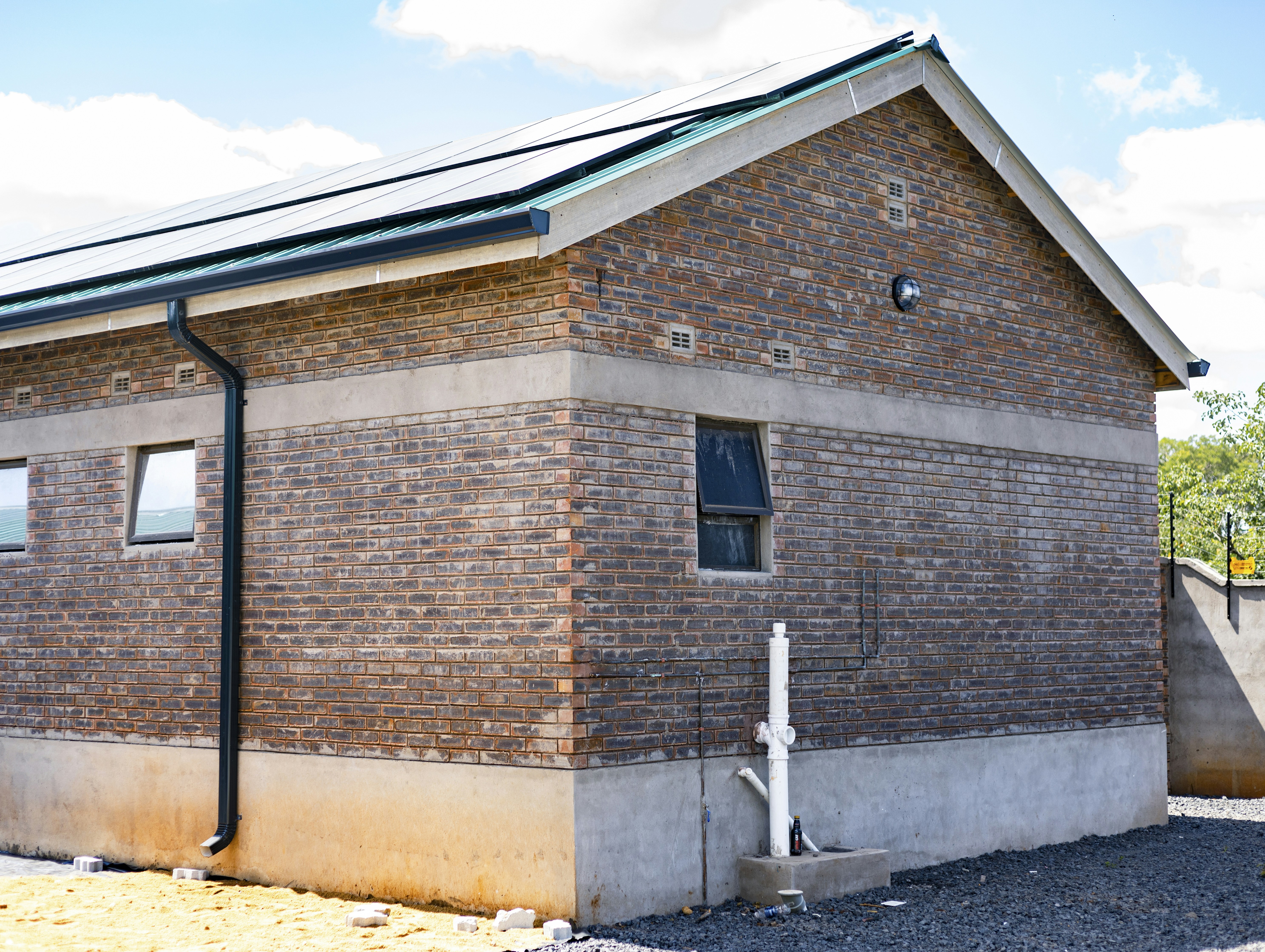 Brick House Under Bright Sky with Water Channel and External Pipe Clad in Shadows
