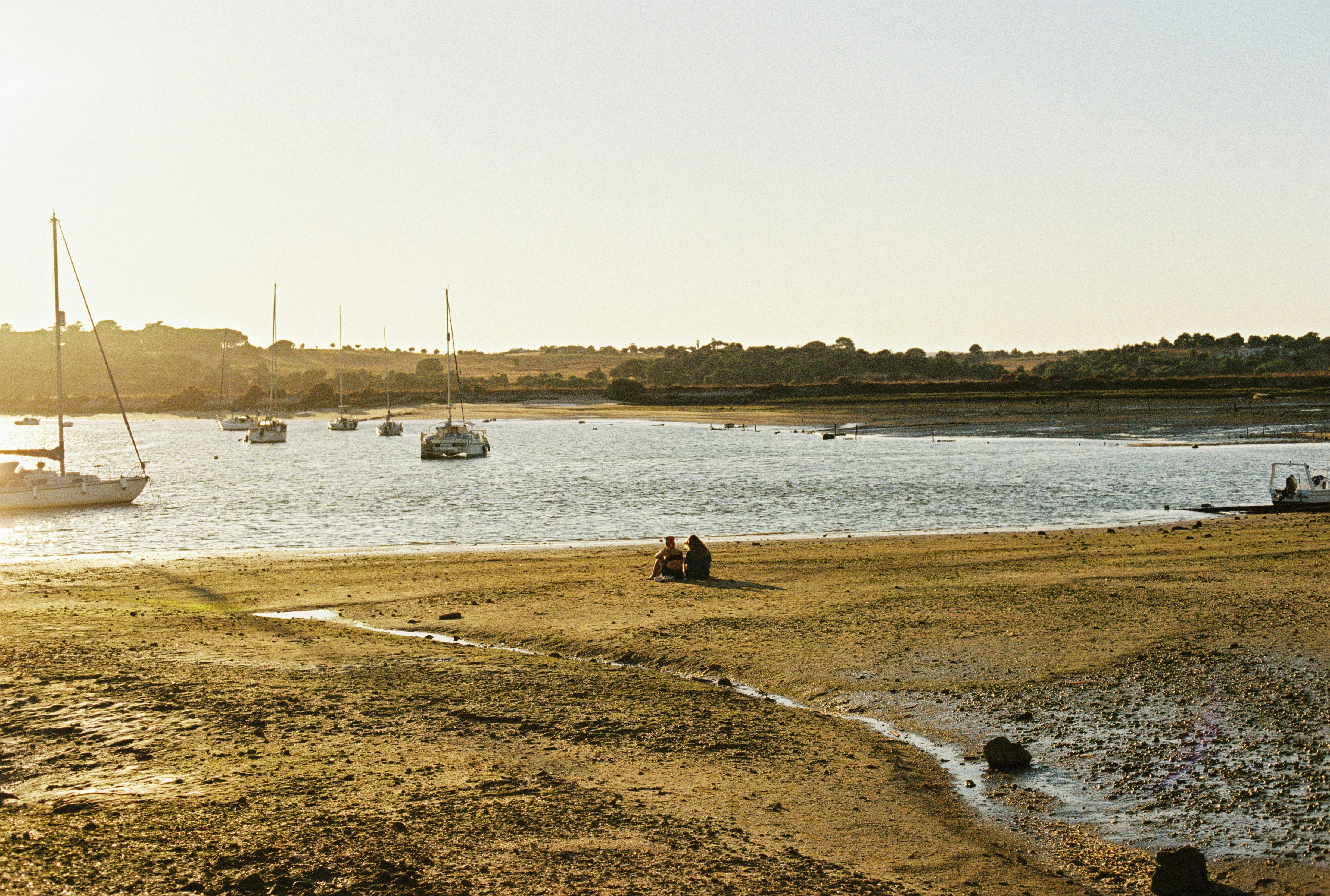 Sunlit shoreline with distant boats and a quiet gathering