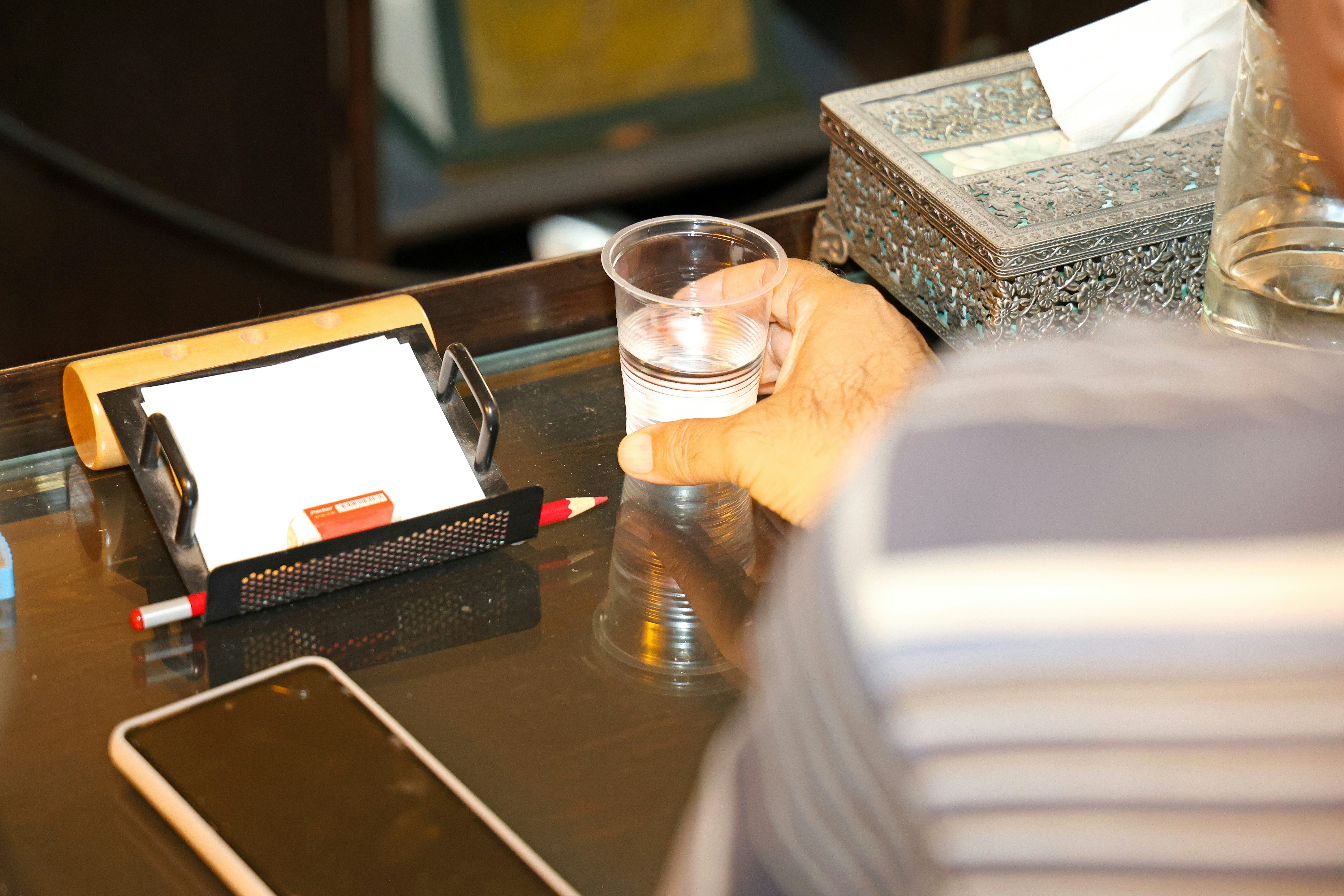 A person holding a plastic cup of water at a desk with stationery