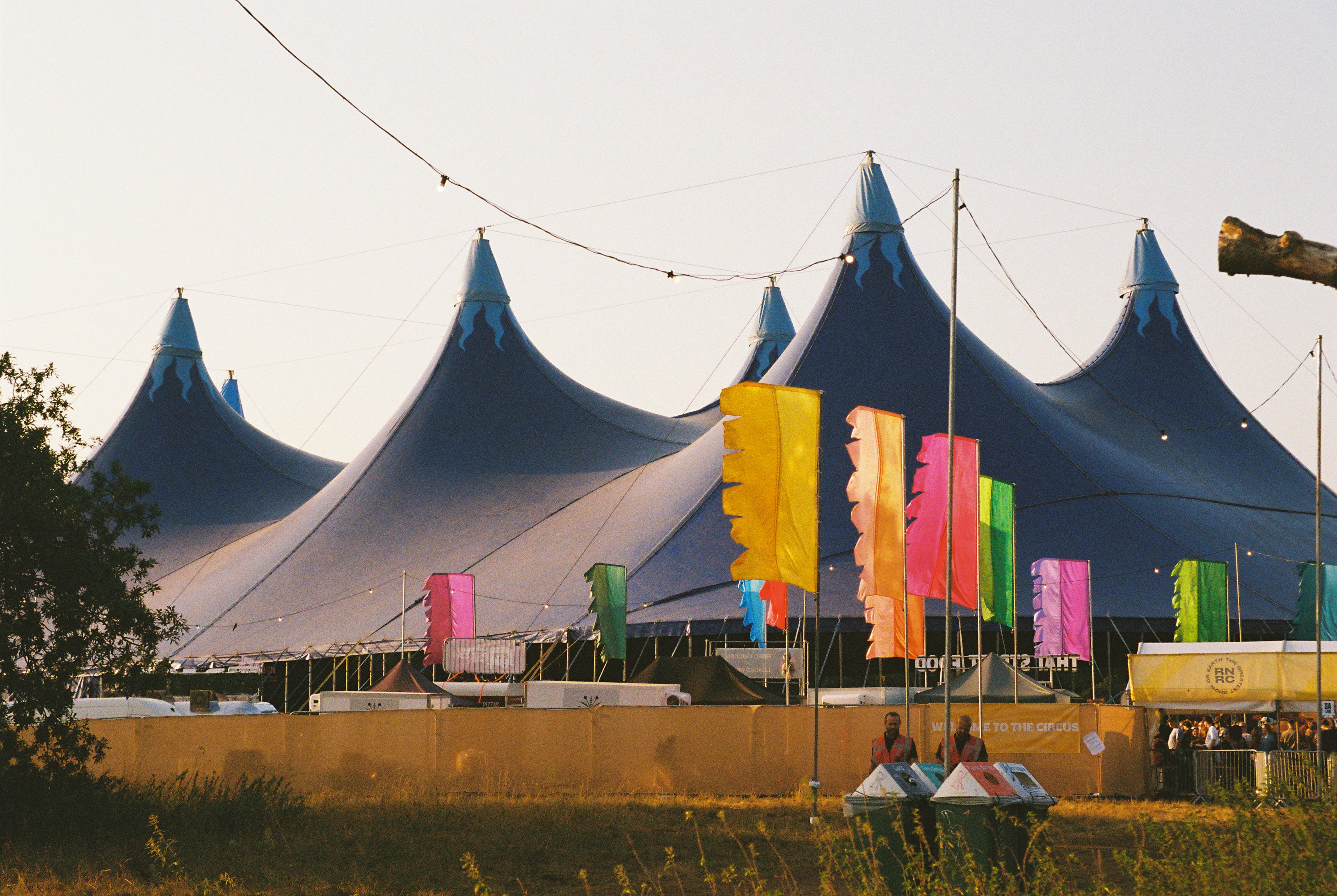 Colorful Banners and Blue Canopy Peaks at a Festival Grounds