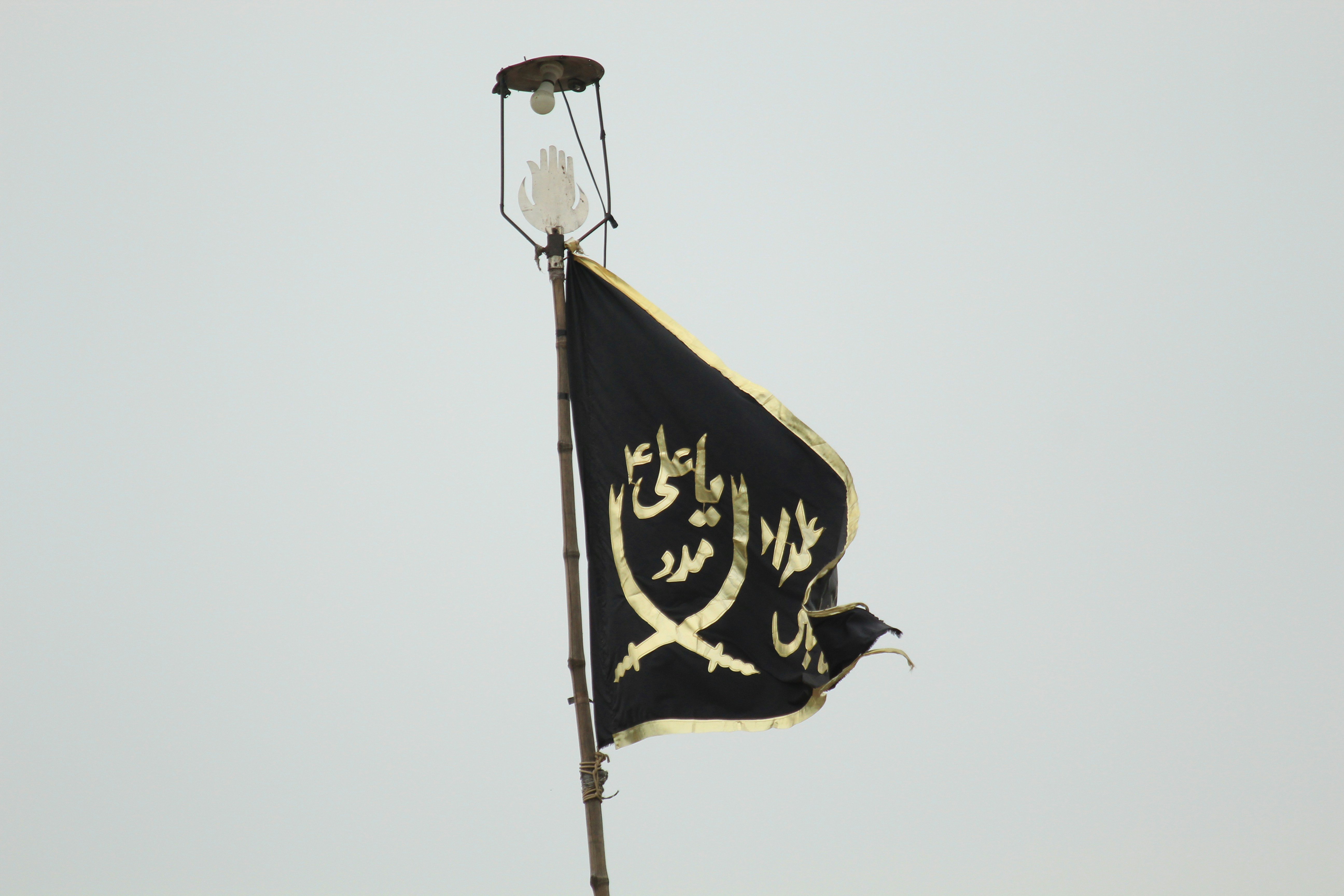Black flag with golden Arabic script waving against a pale sky