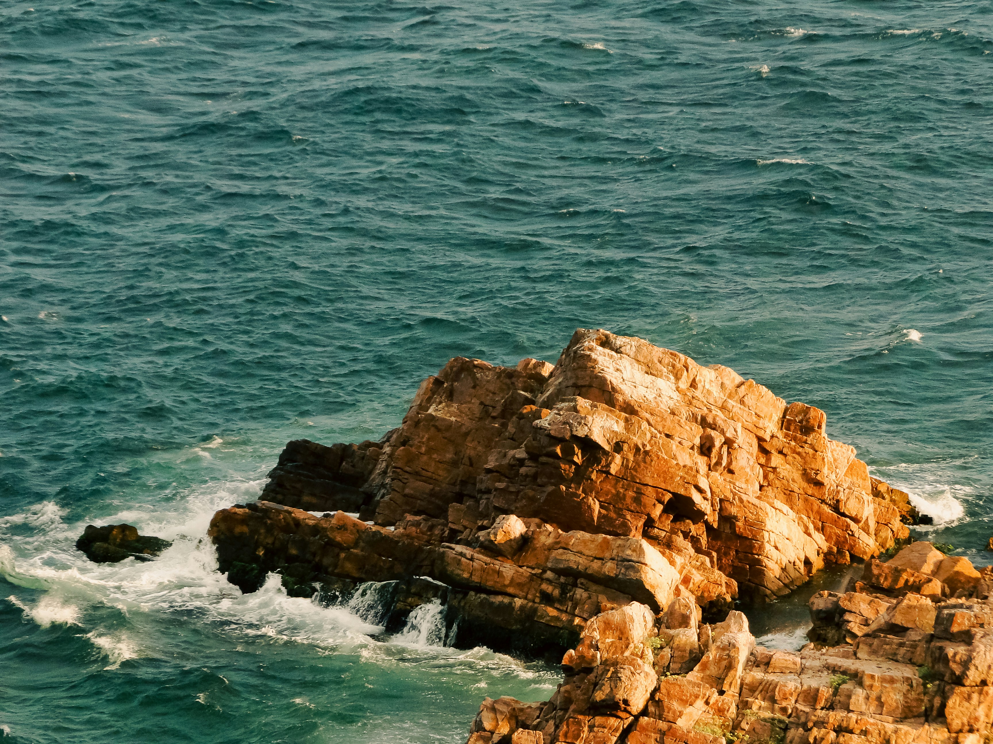 Rugged coastal outcrop basking in teal-green sea light