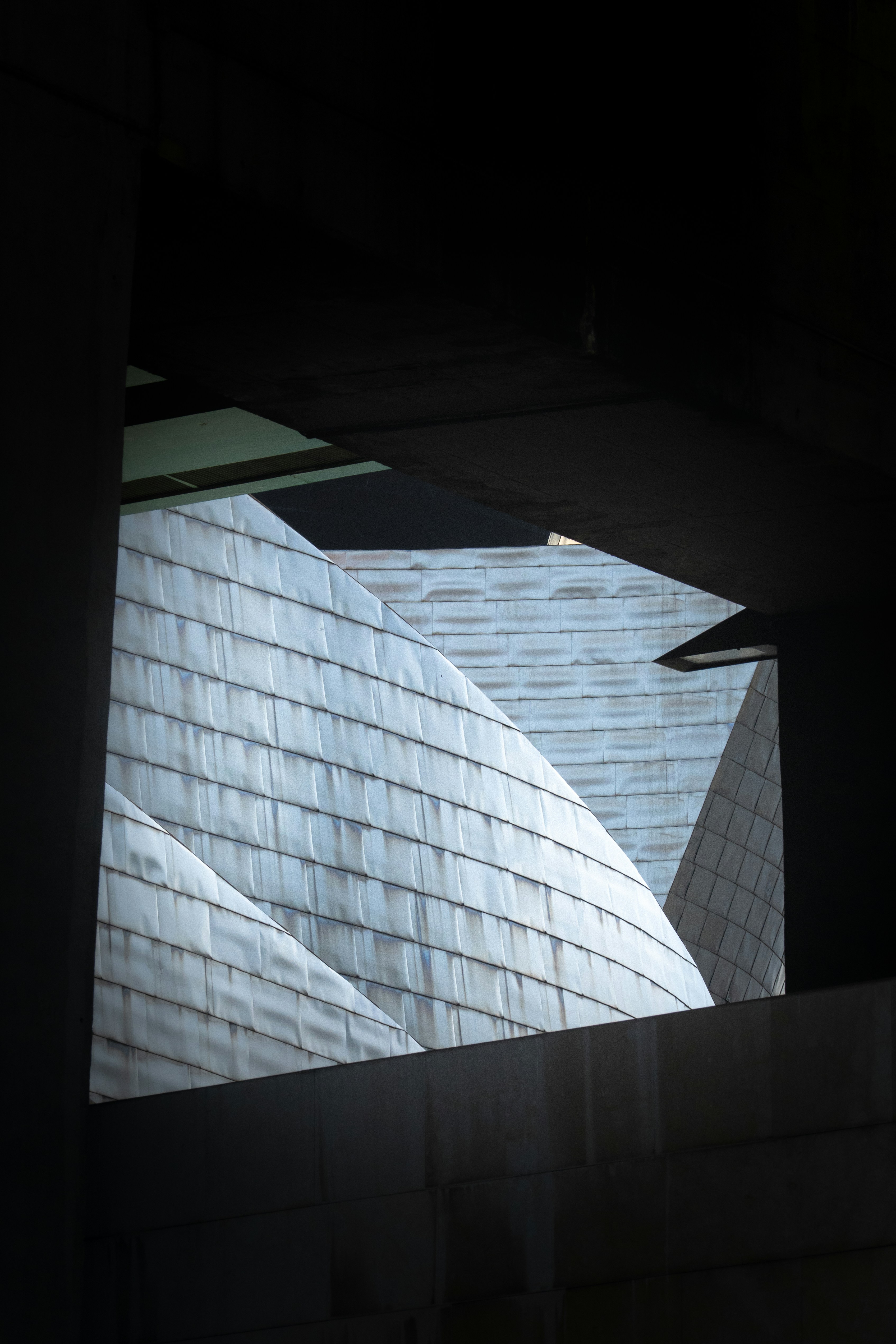 Geometric concrete and slate surfaces form a sculptural composition illuminated by soft daylight, revealing layered planes and sharp edges with high contrast.