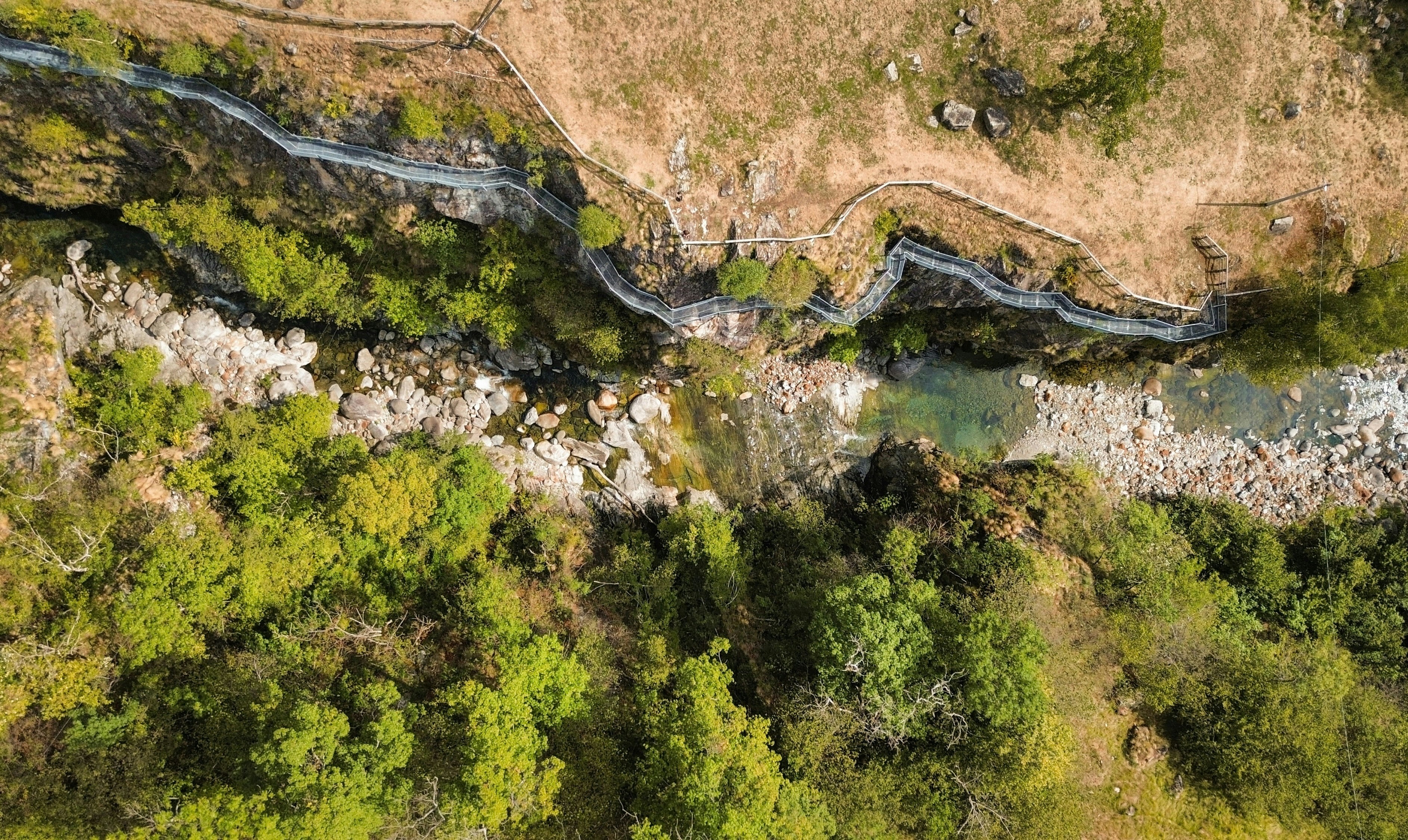 River Vein: Aerial Cliffside Path Through Green and Gravel