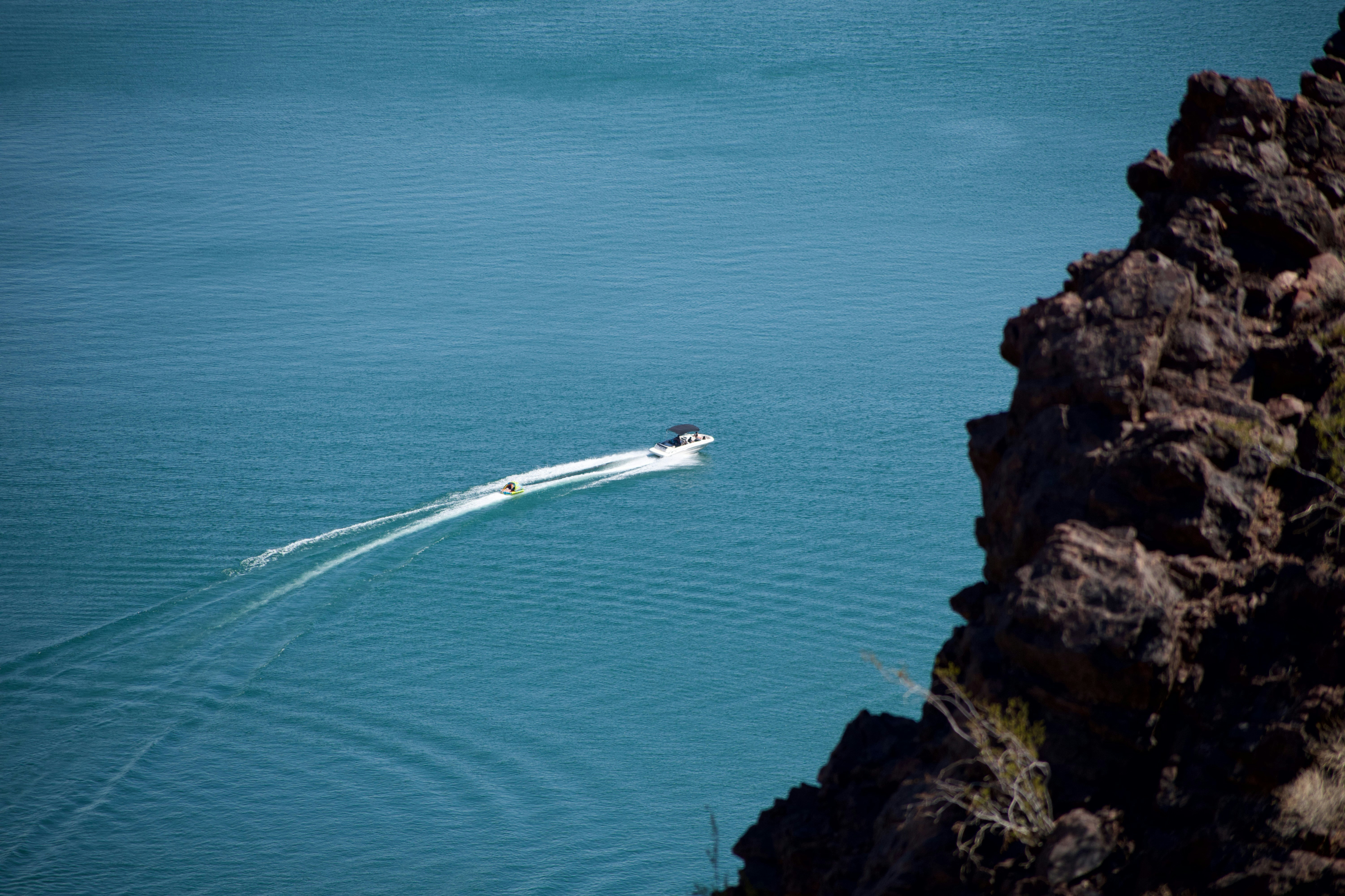 A lone speedboat traces a white wake along azure depths beside rugged volcanic cliffs