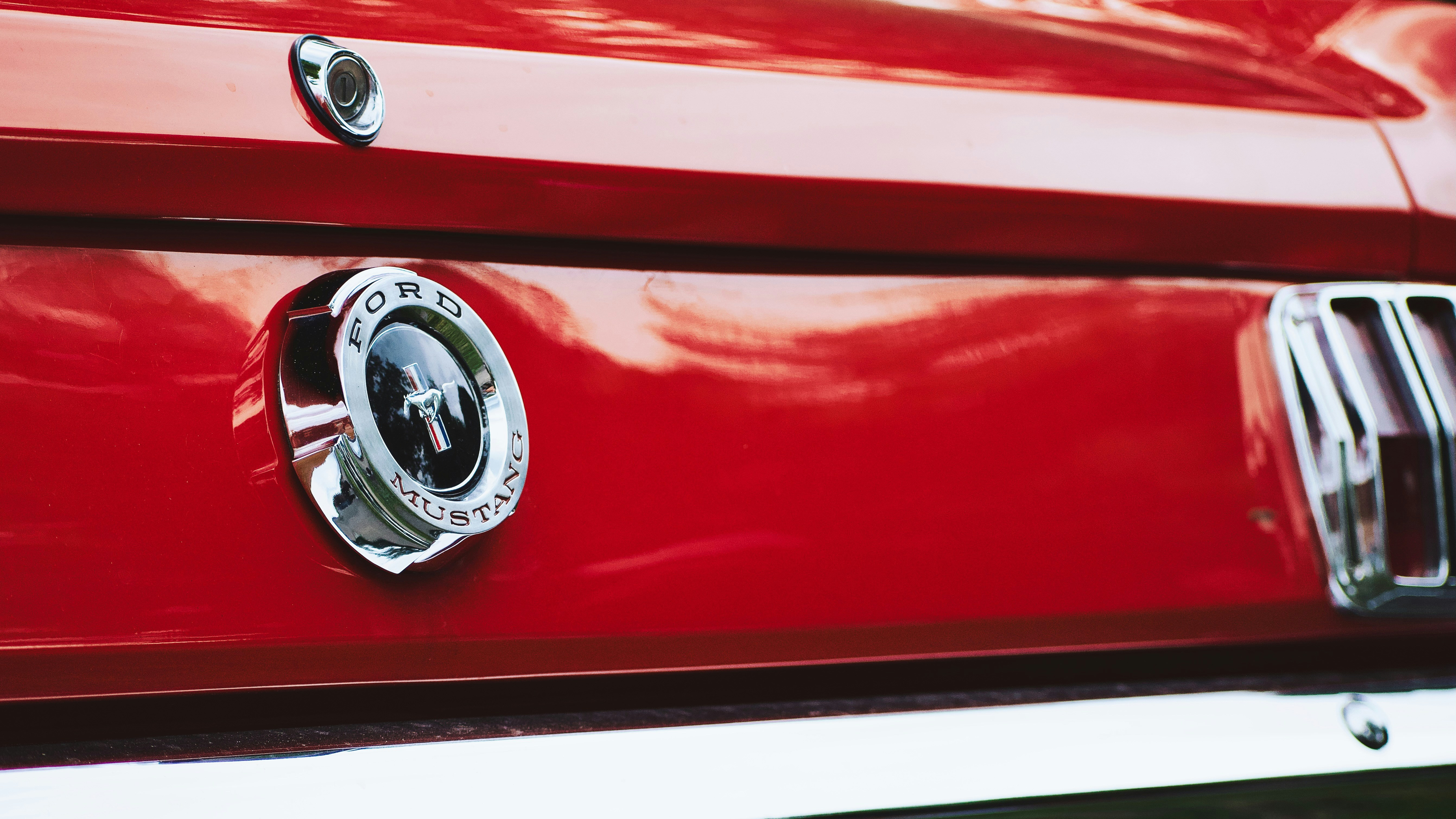 Red Mustang Emblem in Focus: Chrome Detail and Paint Mirroring the Horizon