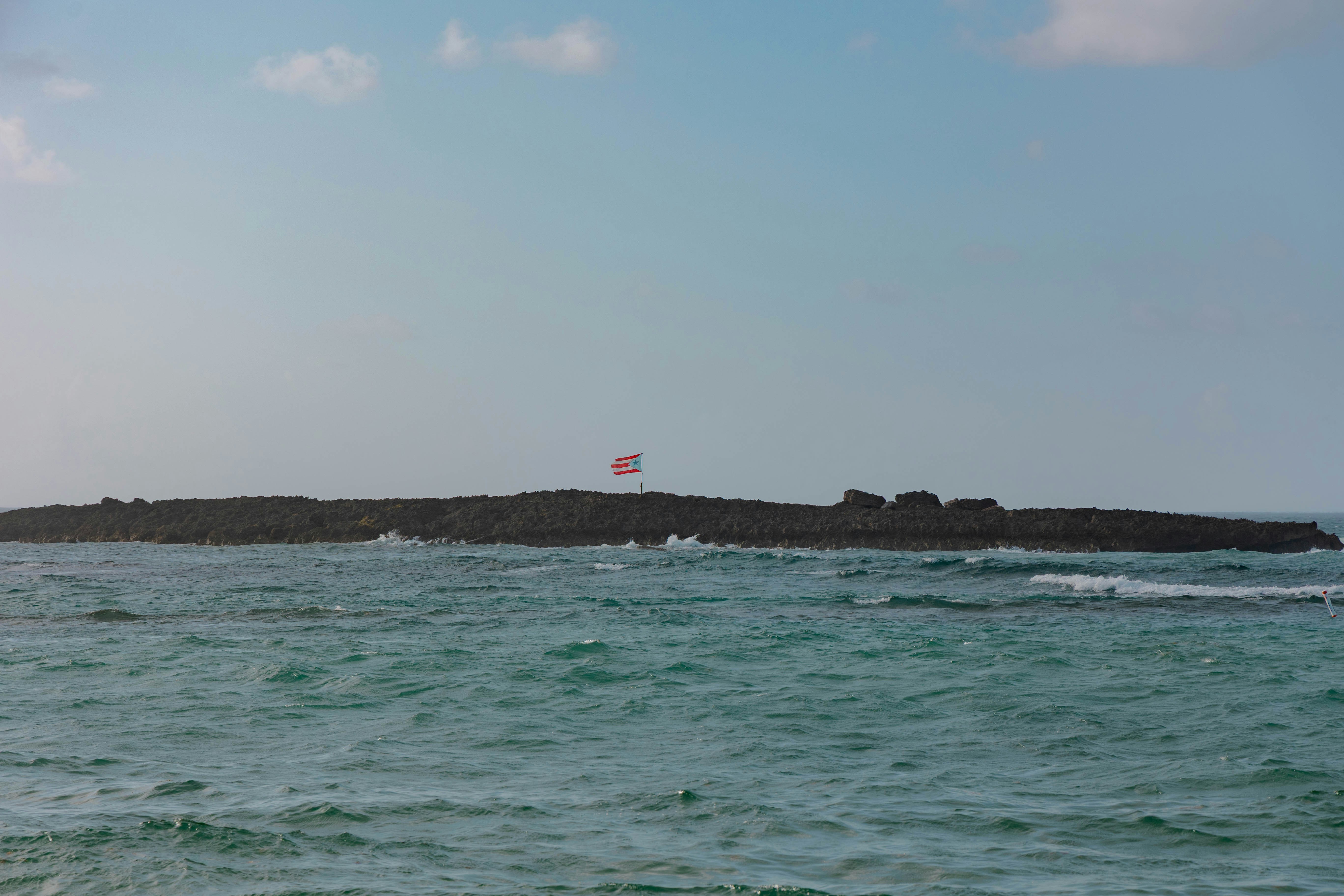 Flag on a distant breakwater: quiet horizon over turquoise waters