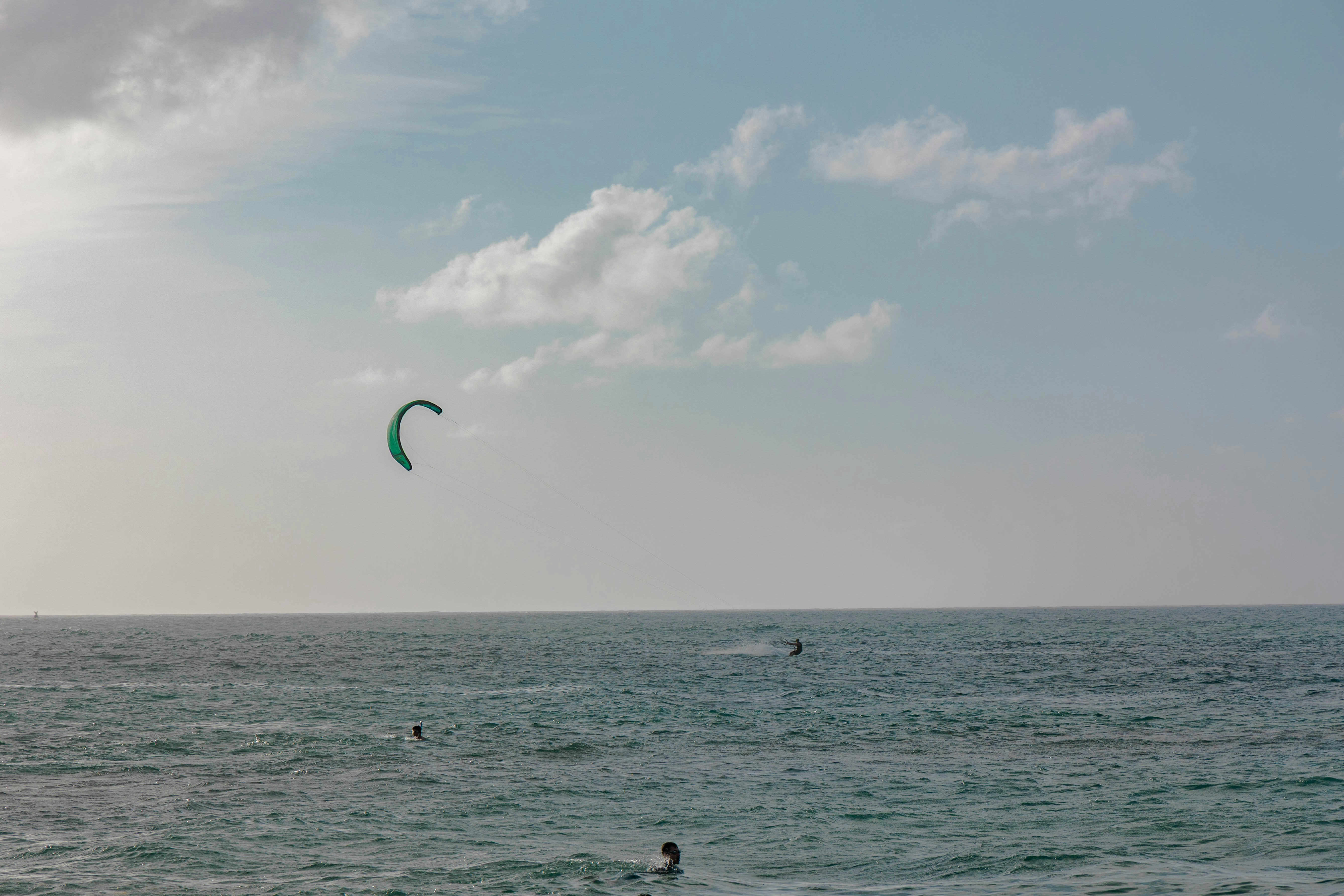 A person kitesurfing with a green kite over the ocean under a cloudy sky