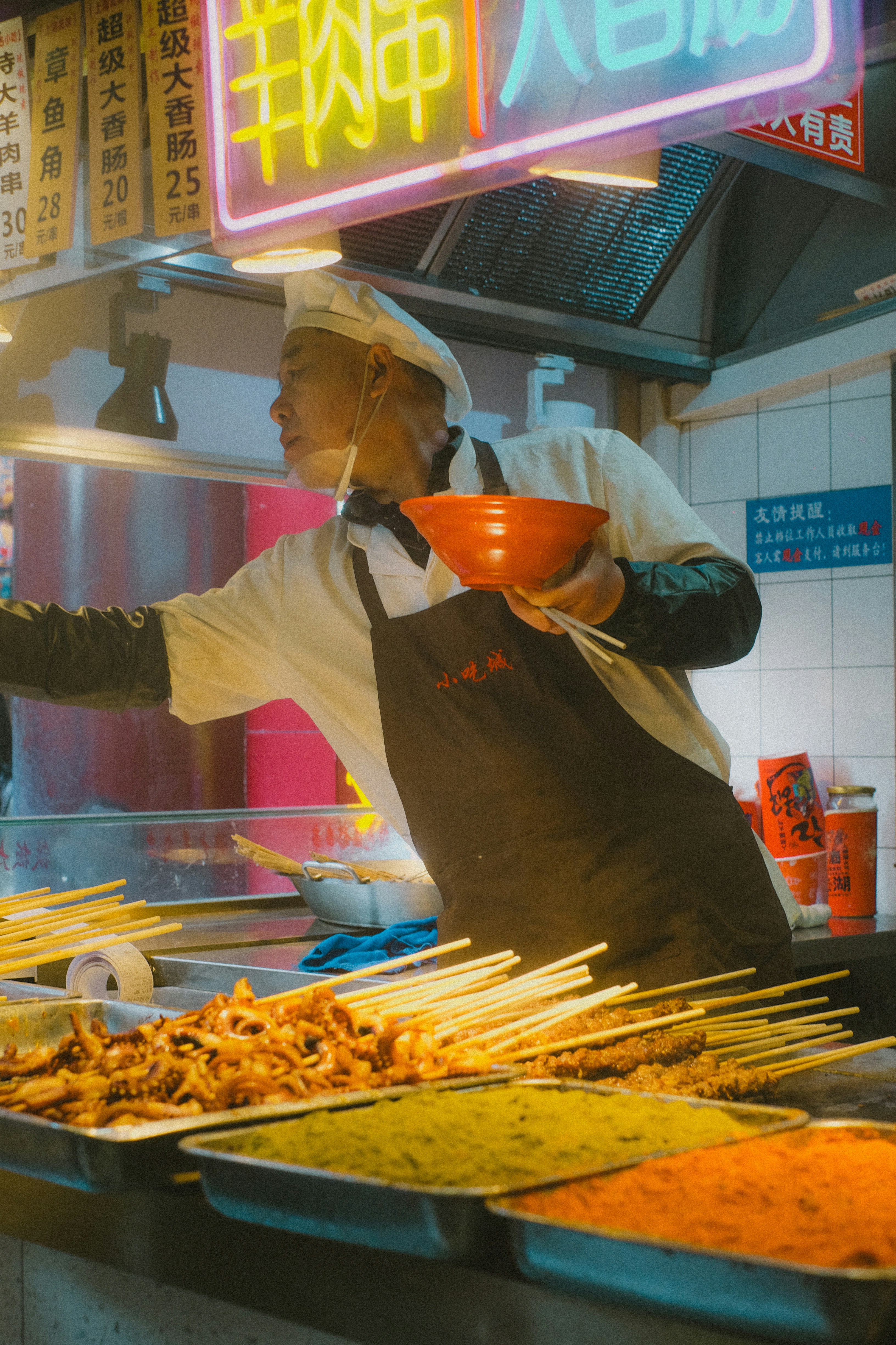 Vendor in Neon Glow Serving Noodle Skewers Under Street-Side Heat