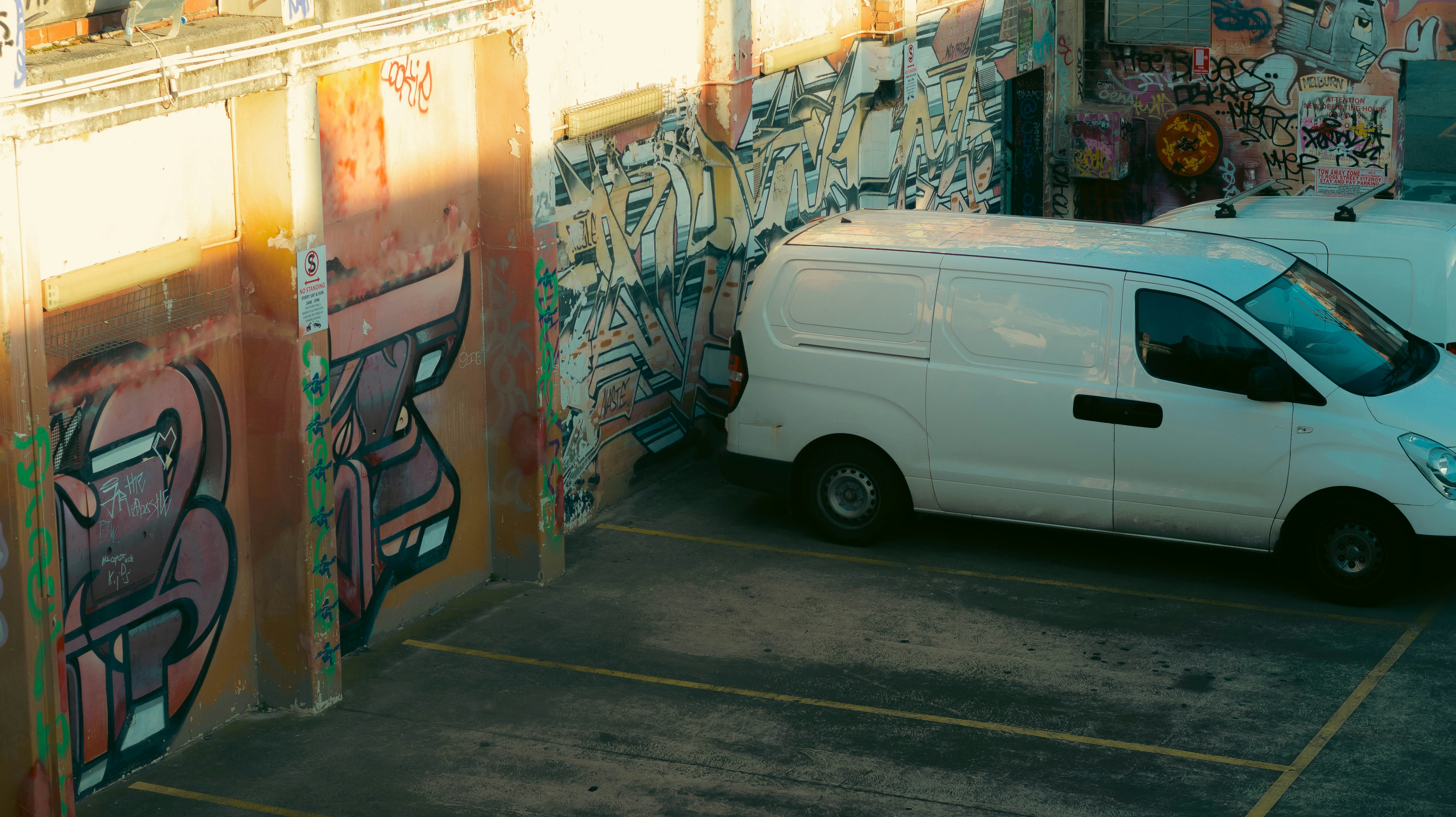 White cargo van parked in a graffiti-covered alley, sunlit concrete and yellow parking lines in the foreground.