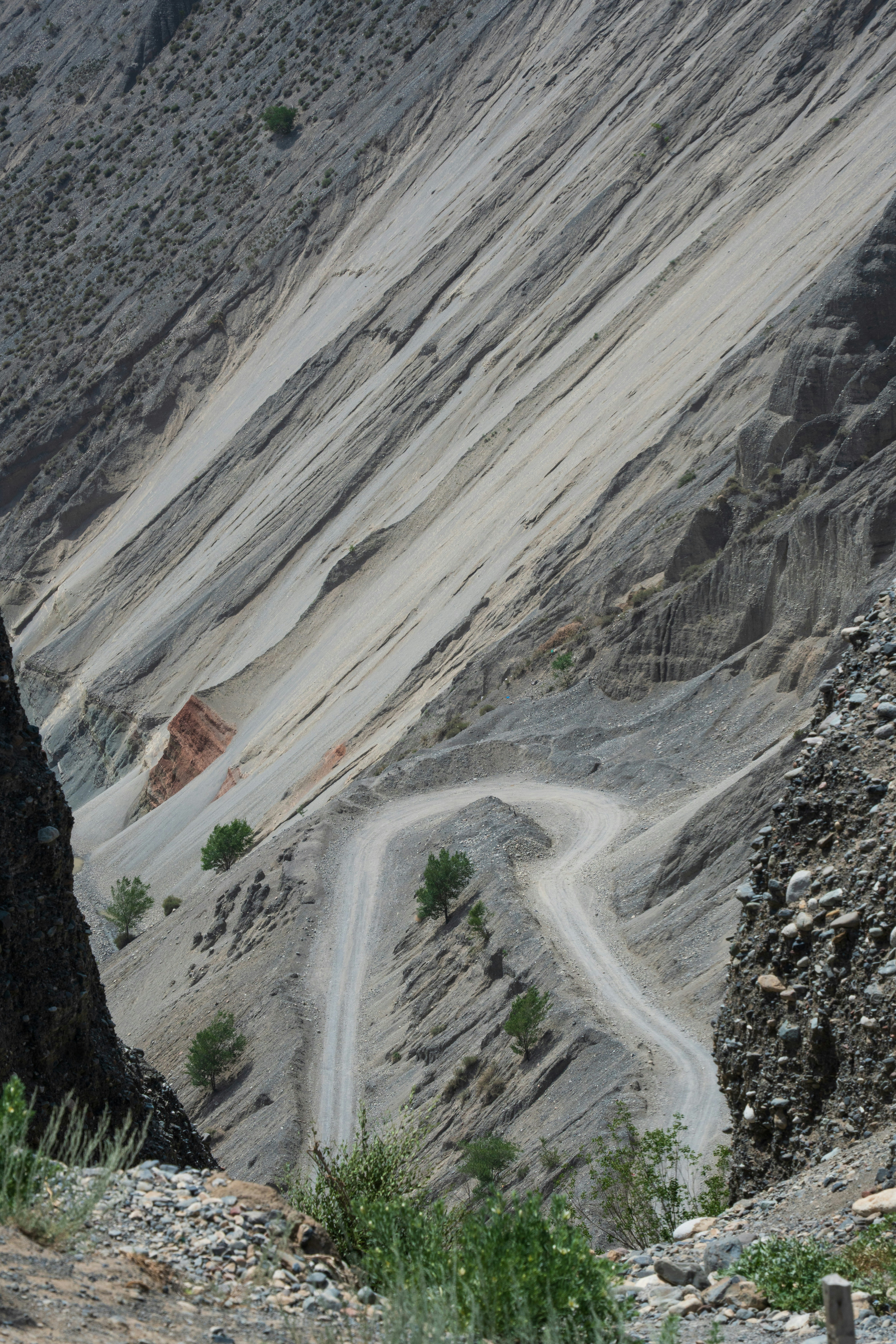A winding, dust-gray canyon road carves its way through towering talus and sparse pines