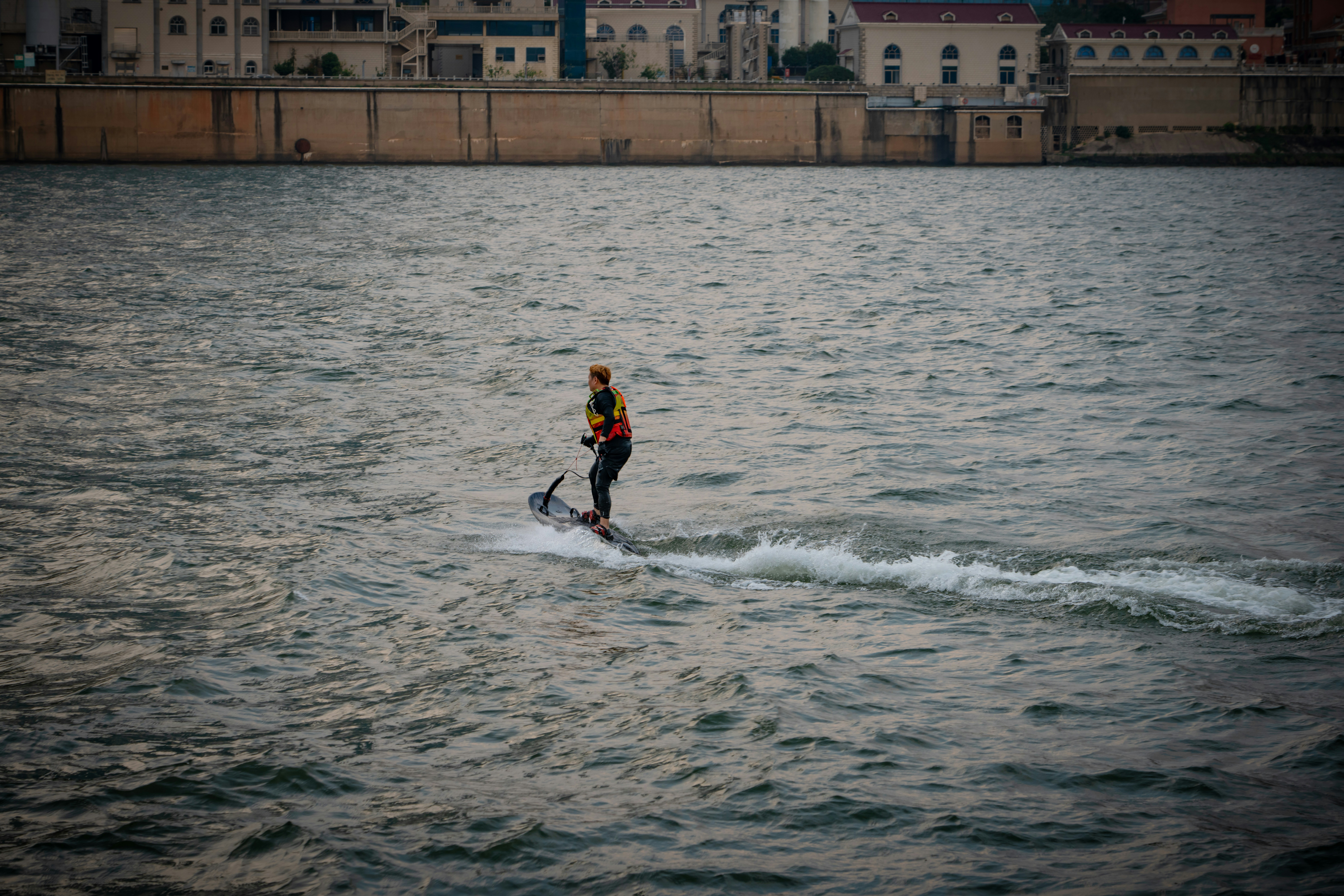 Single Windsurfer Cutting a Wake Past the Distant Waterfront