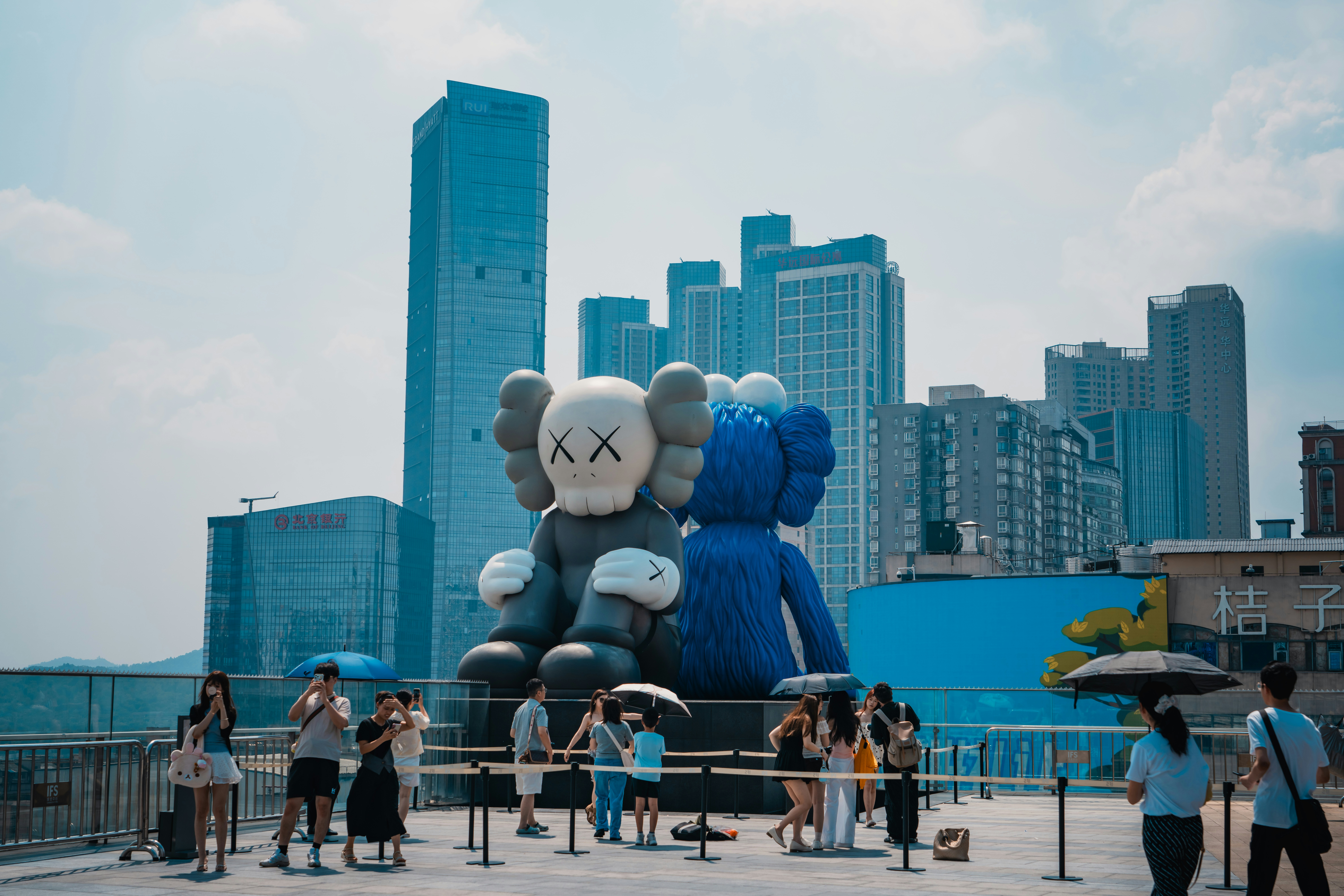 Statues in the Skyline: Iconic KAWS Duo Overlooking a Busy Riverside Walk