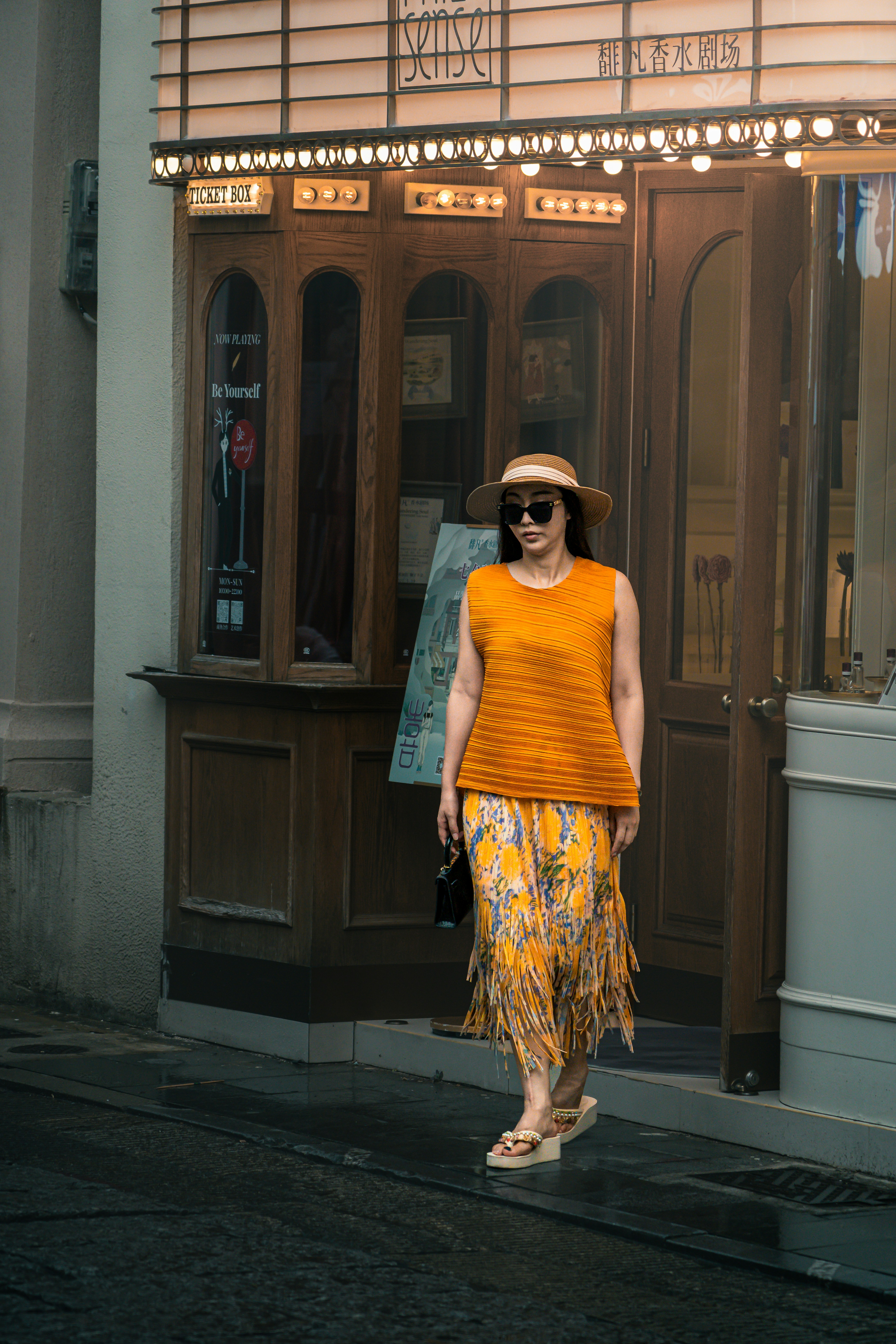 Sunlit Chic: A Woman in Orange by a Vintage Theater Facade