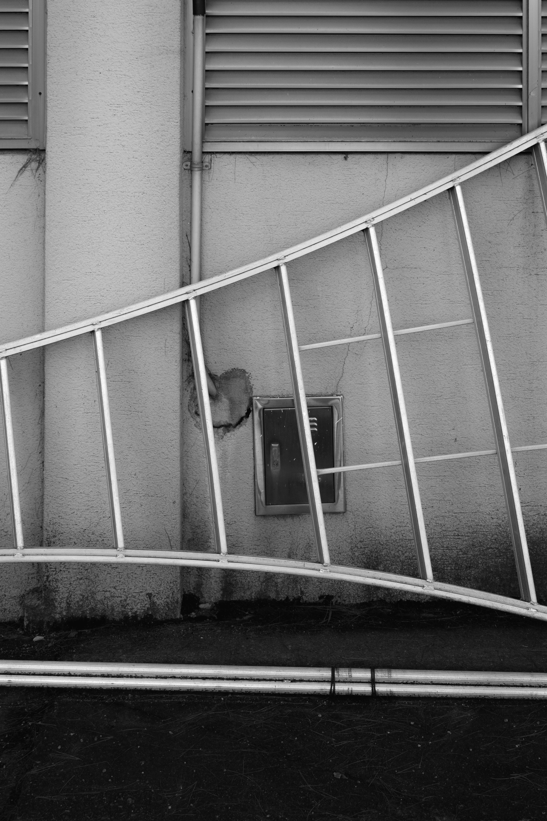 A Broken Tilt: Curved Rail Against a Concrete Facade