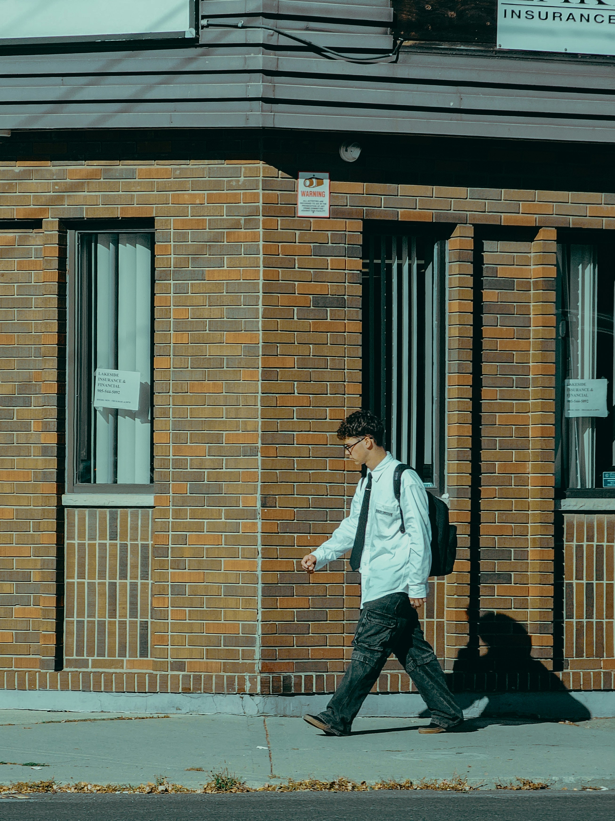 A lone commuter strides past brick storefronts into the afternoon light