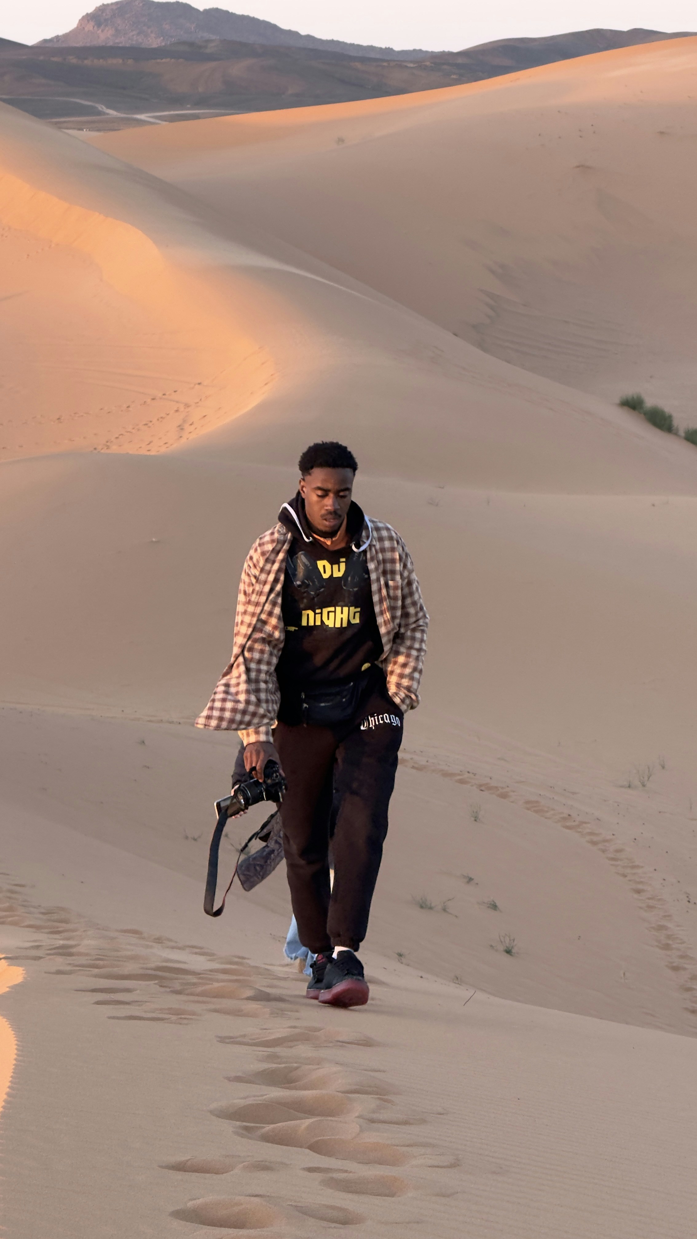 Desert Walk: A Lone Photographer Traverses Dune Peaks at Dusk