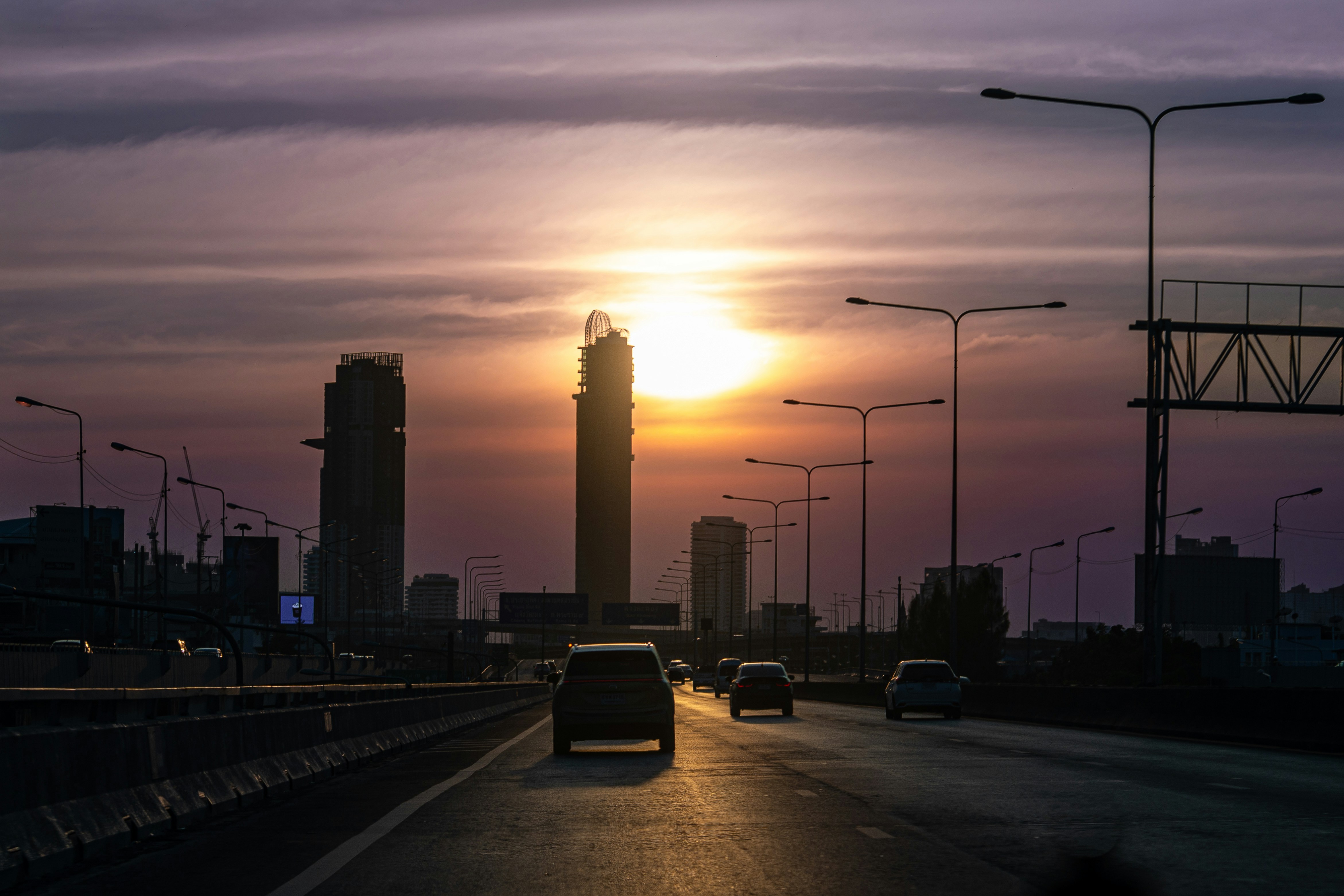 Golden hour highway traffic heading toward the Bangkok skyline silhouette at sunset