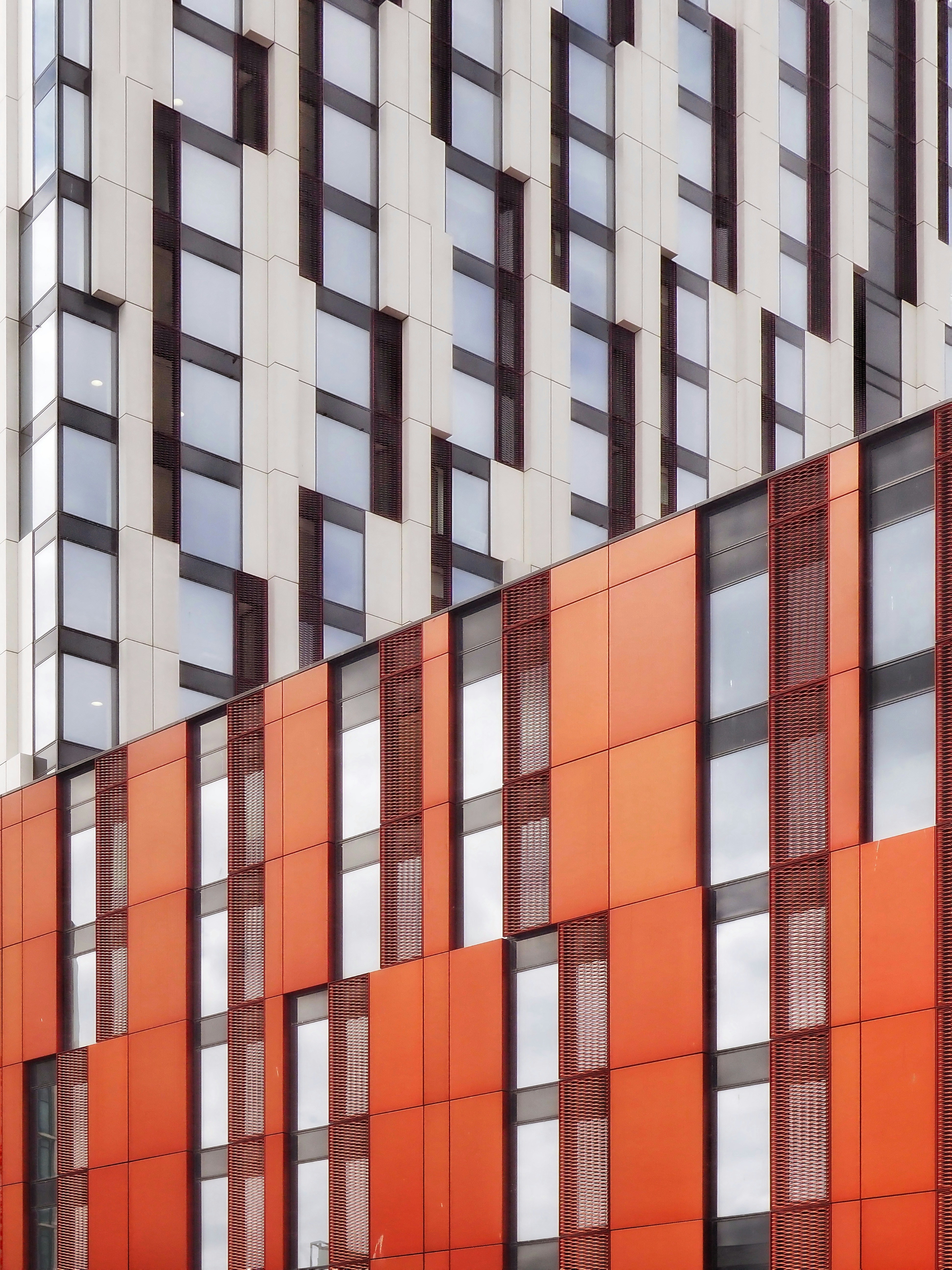 Orange-and-gray urban cladding with alternating window panes forming diagonal geometry against a pale vertical backdrop. Architectural detail emphasizing color blocks and rhythm.