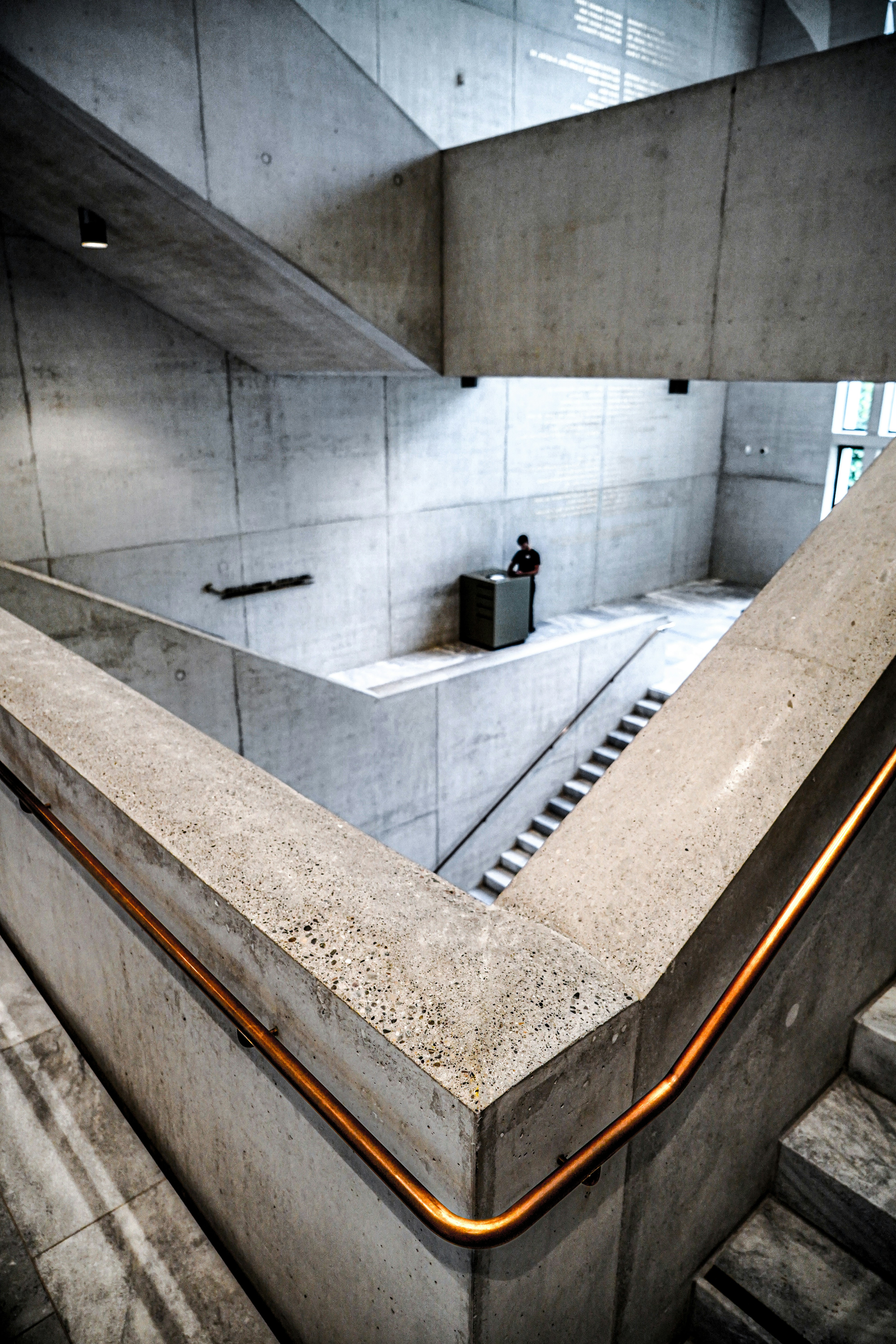 Concrete Atrium: A lone figure and the geometric labyrinth of stairs