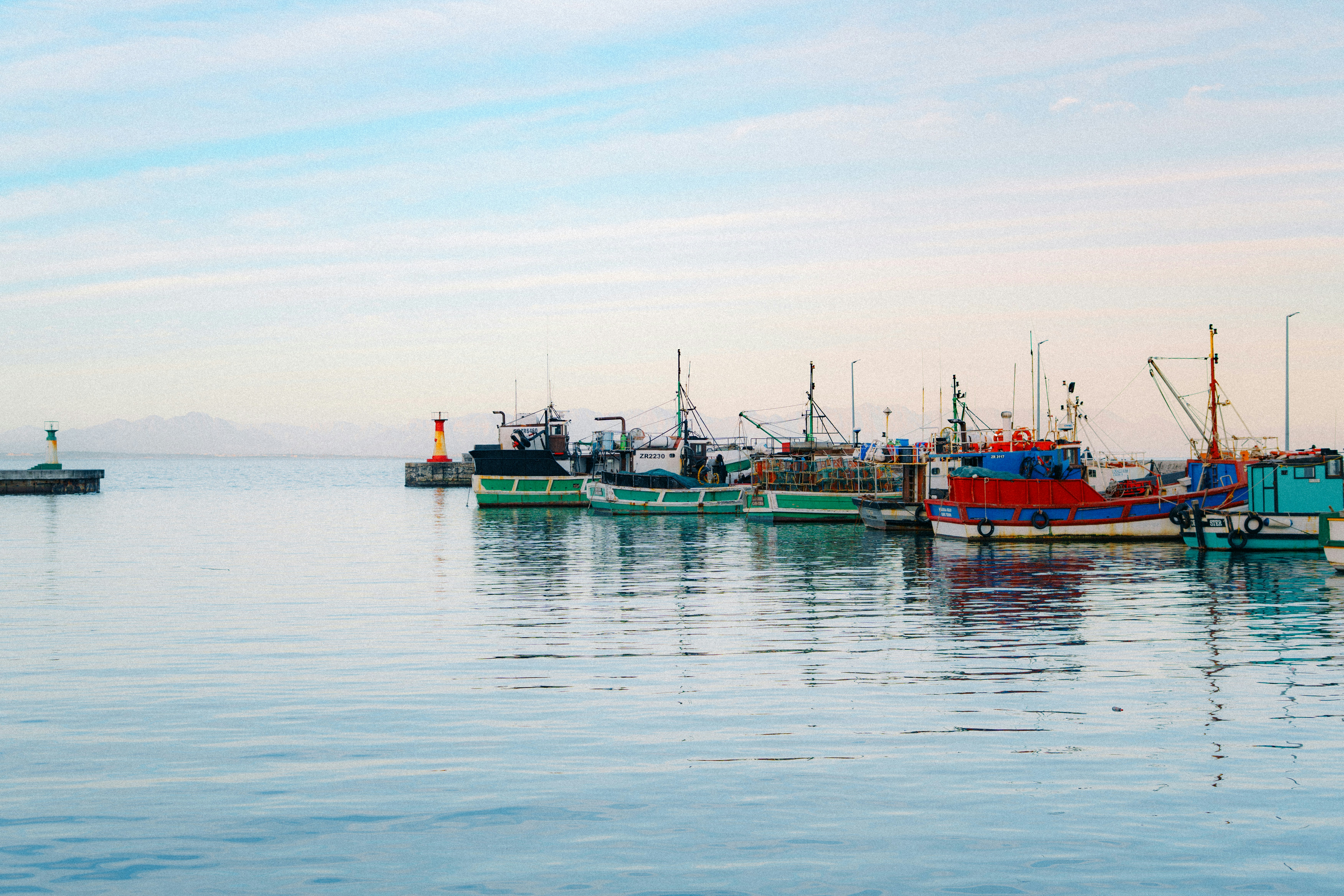 Colorful fishing boats docked along a calm harbor with soft reflections on the water.