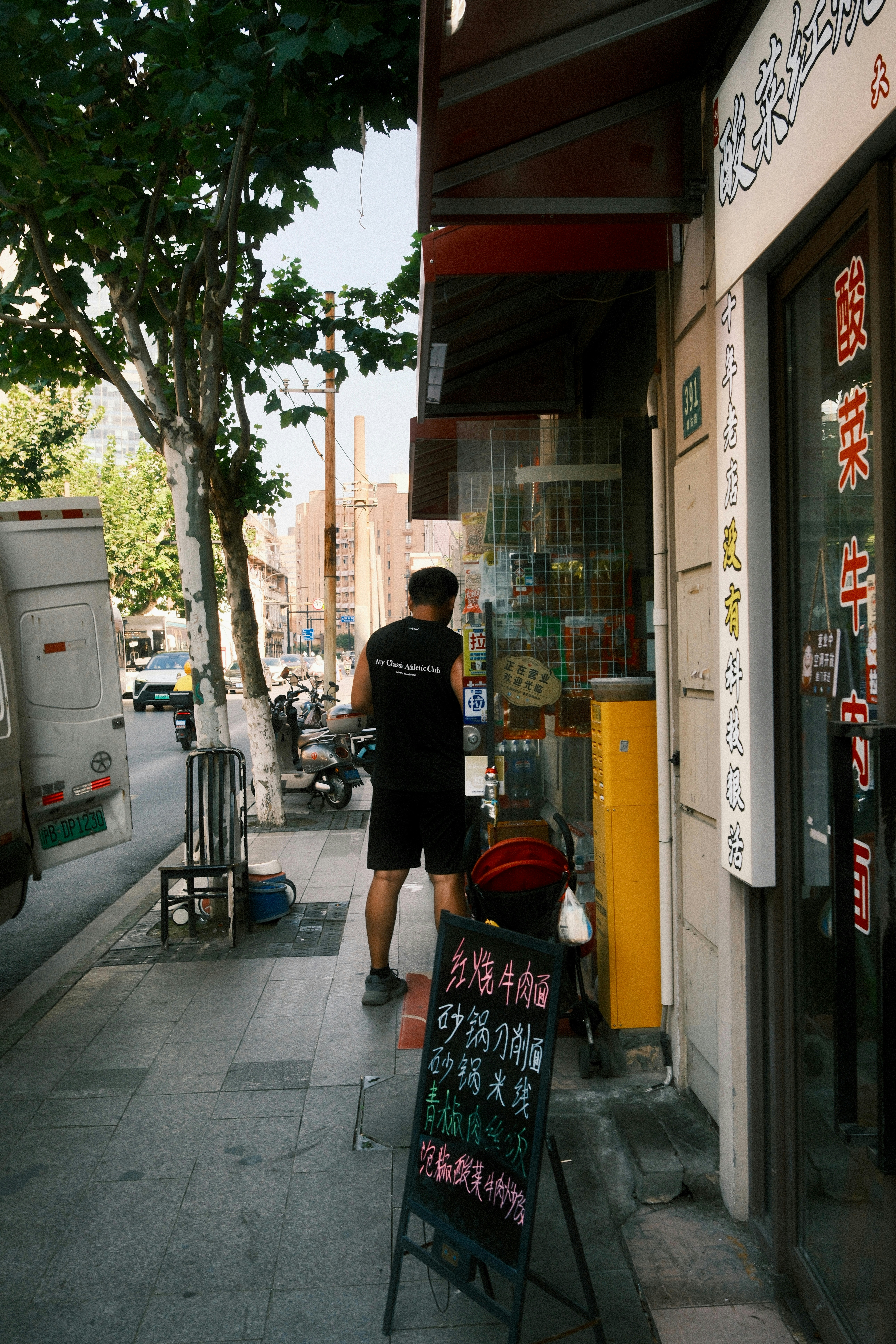 Street-side routine: a man in black pauses outside a shop as signs glow with Chinese characters