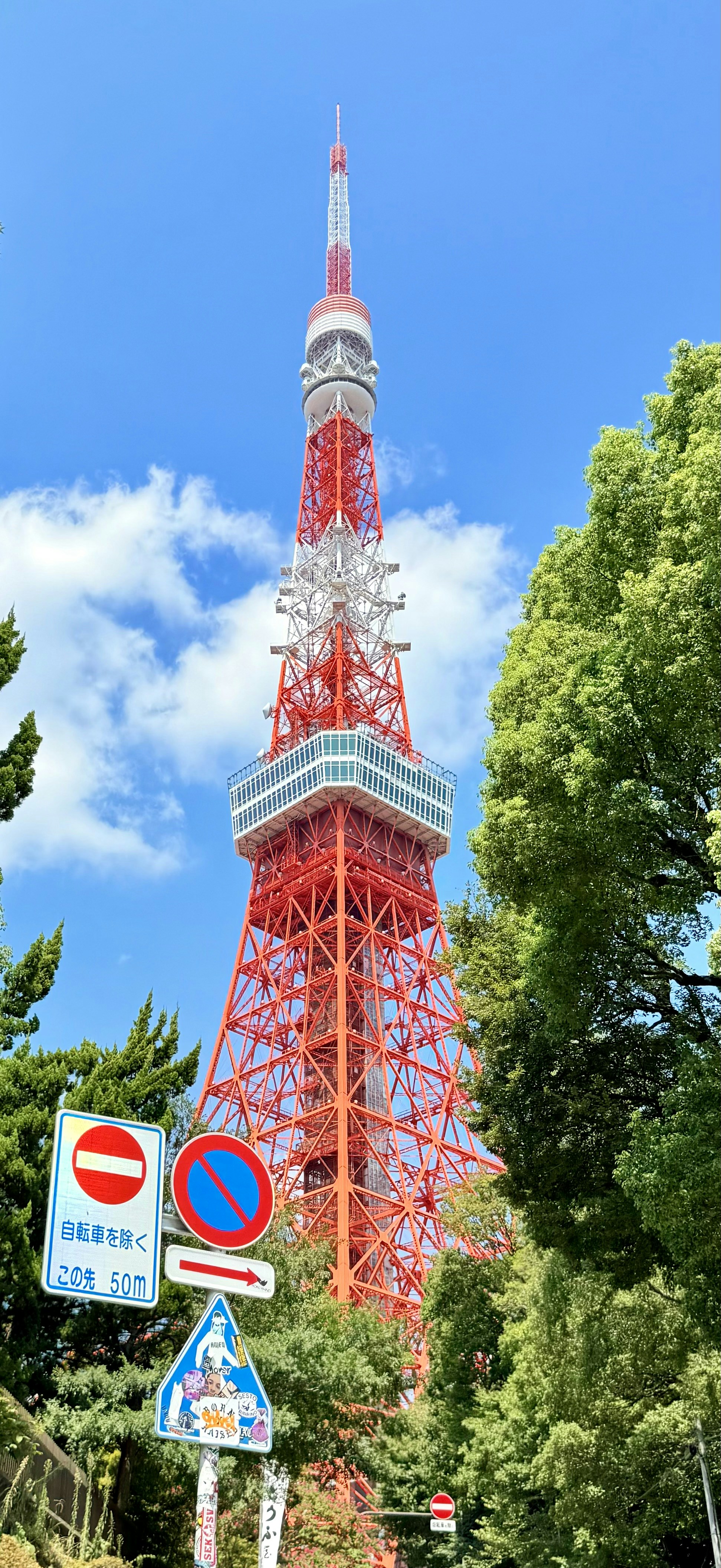 Tokyo Tower reaches toward a clear summer sky with bright red lattice and surrounding green trees
