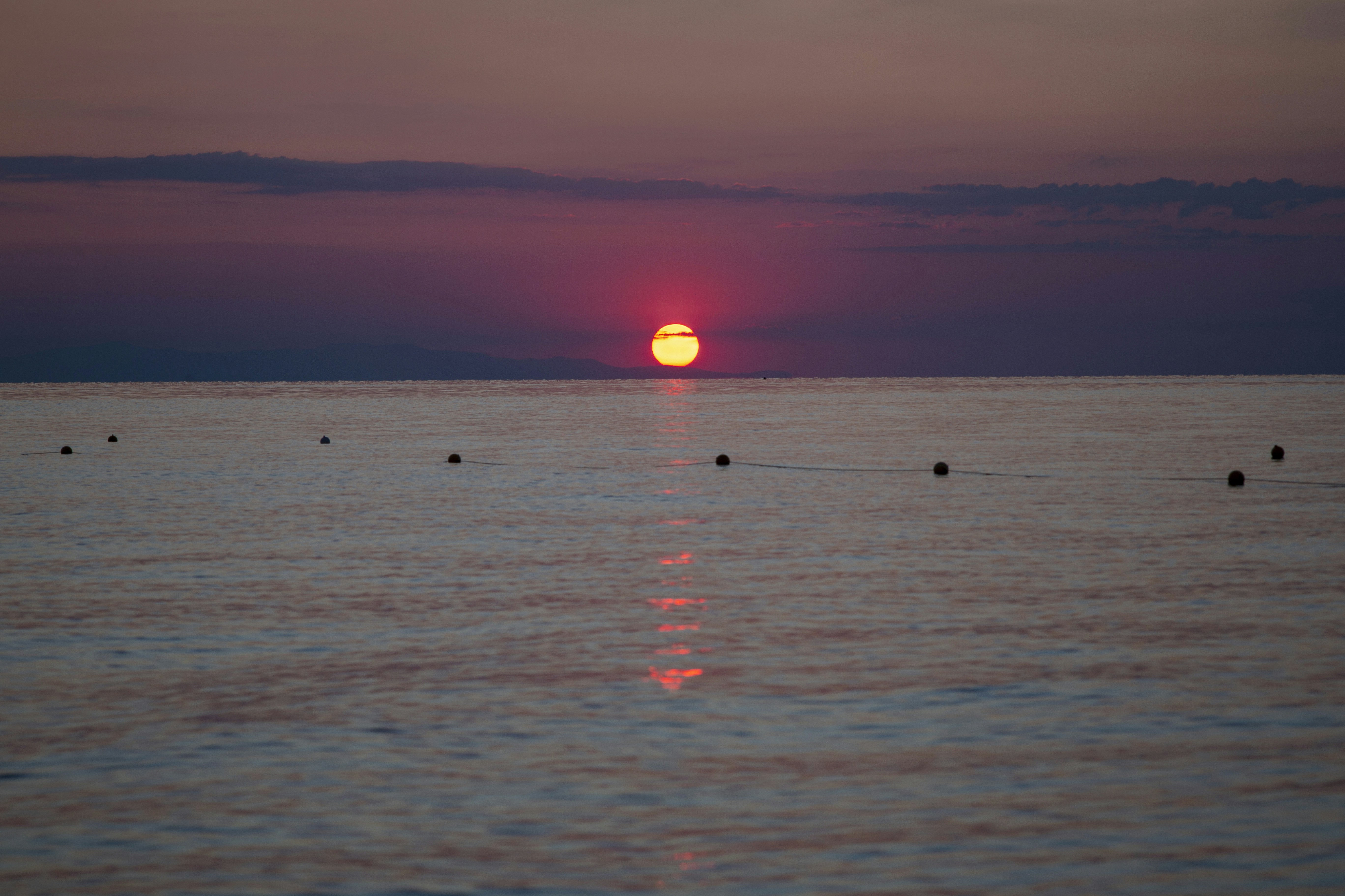 Soft sunset over calm water with a line of buoys along the horizon.