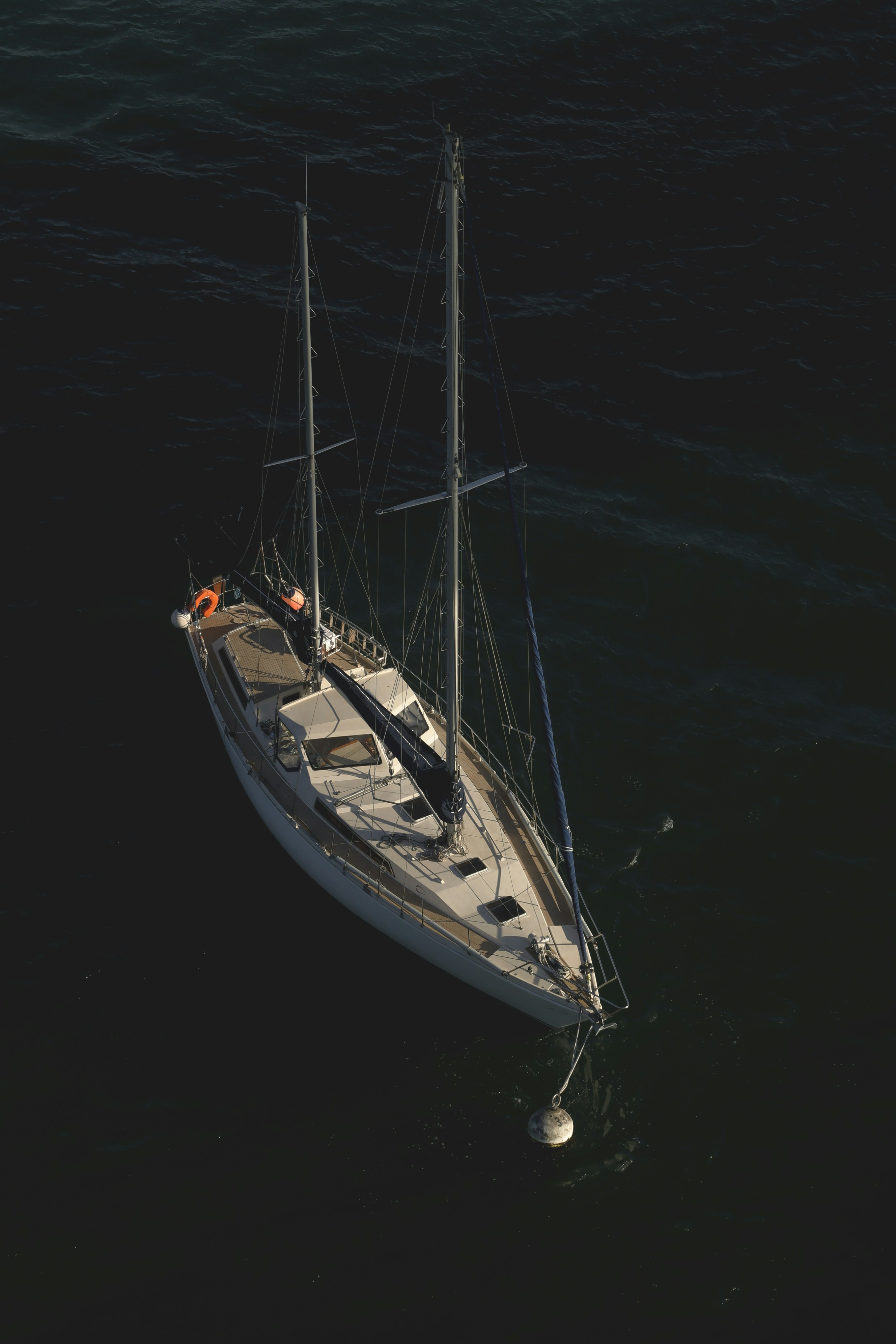 A lone sailboat drifts through dark offshore waters at dusk
