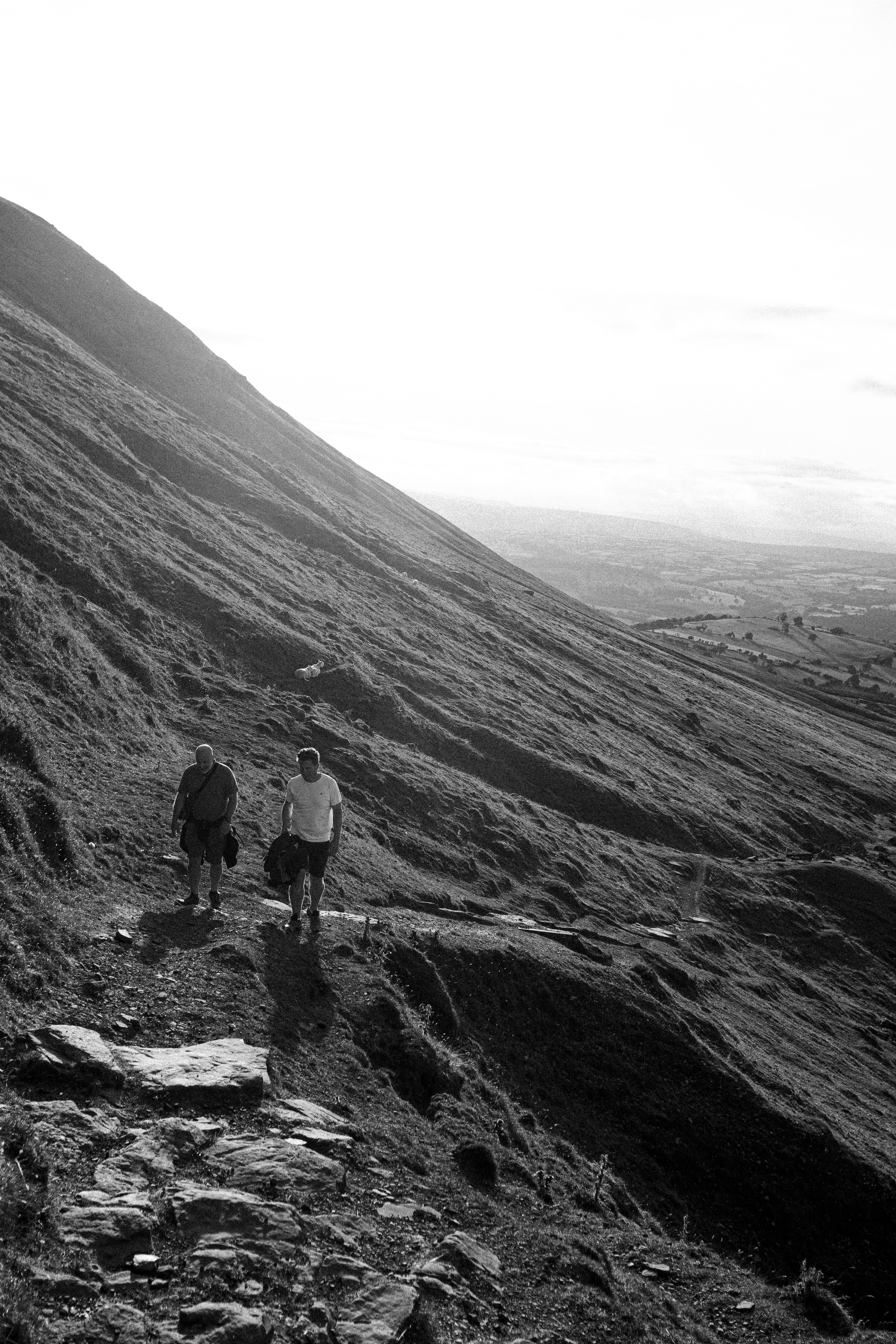 Two hikers ascend a sunlit ridge along a rugged mountainside