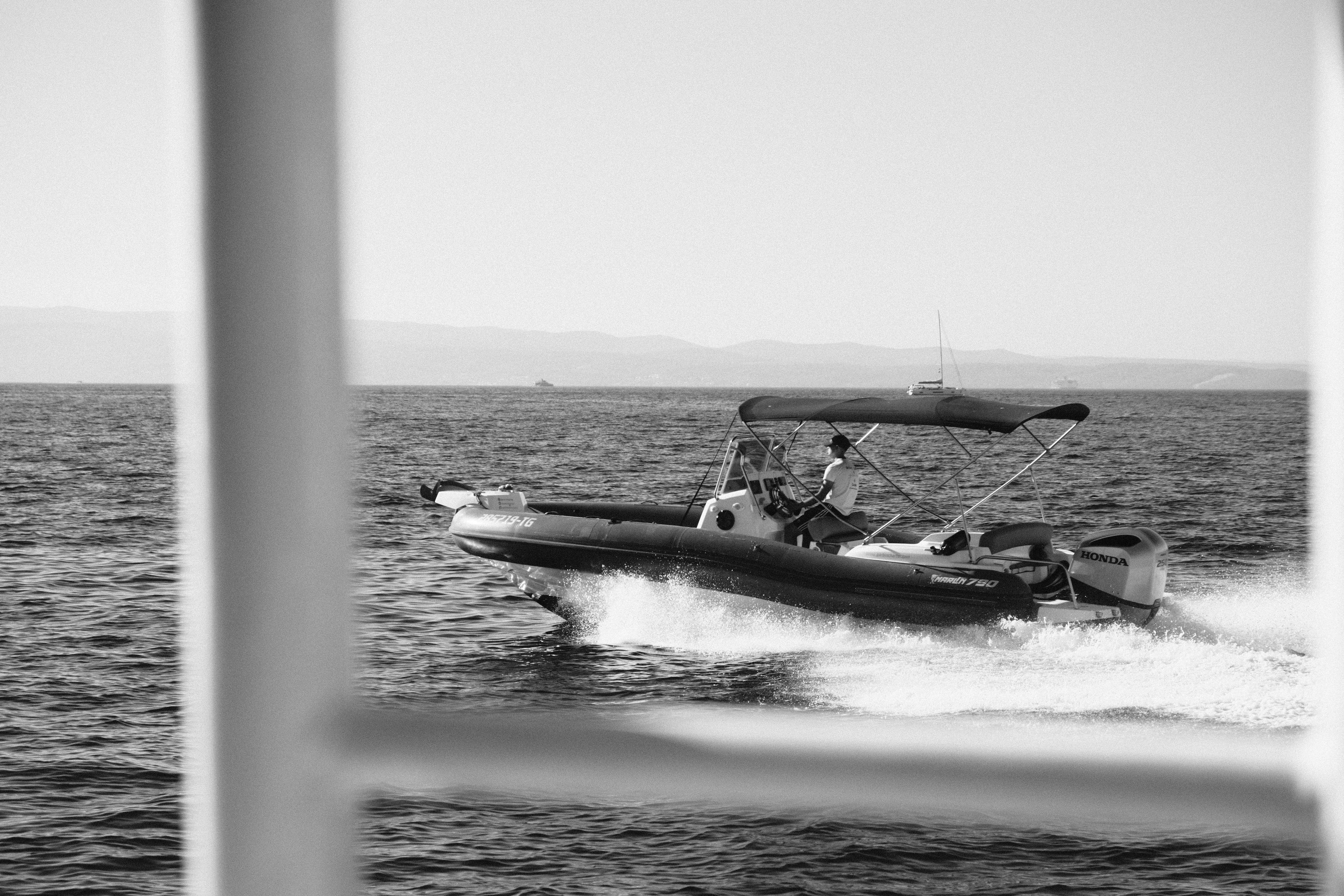 A fast motorboat cuts across choppy water, viewed through a window frame that creates a foreground divider and a sense of motion.