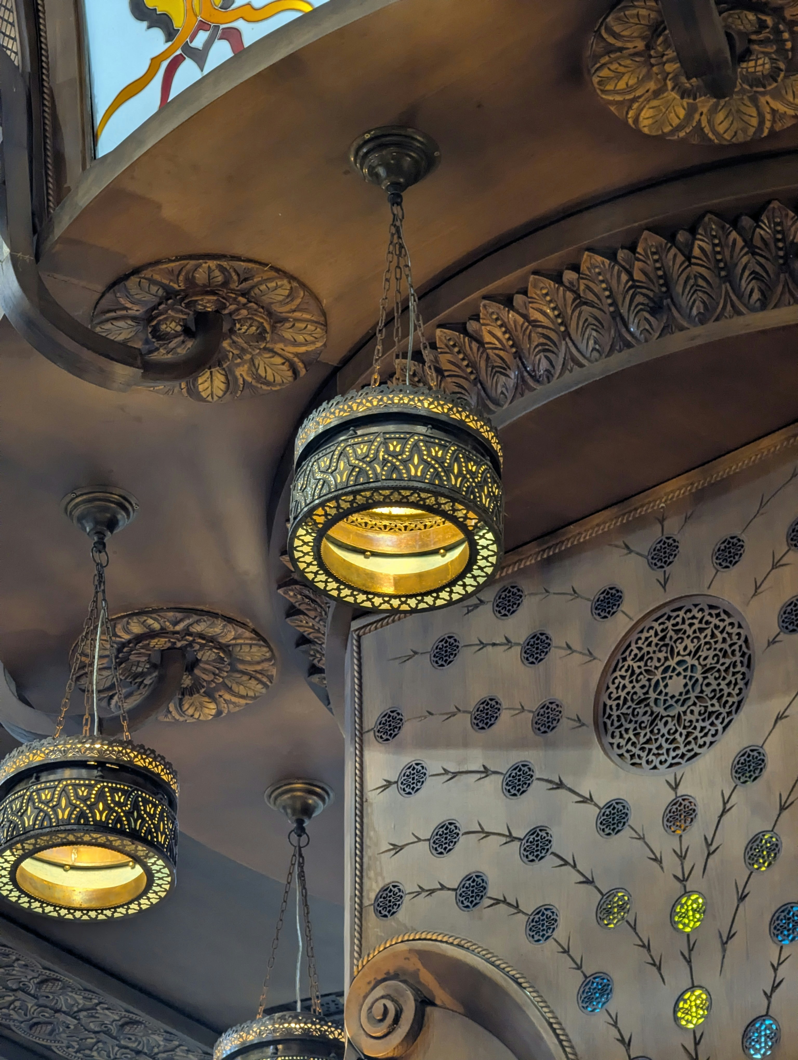 Decorative hanging lanterns illuminate an intricately patterned ceiling with filigree and botanical motifs.