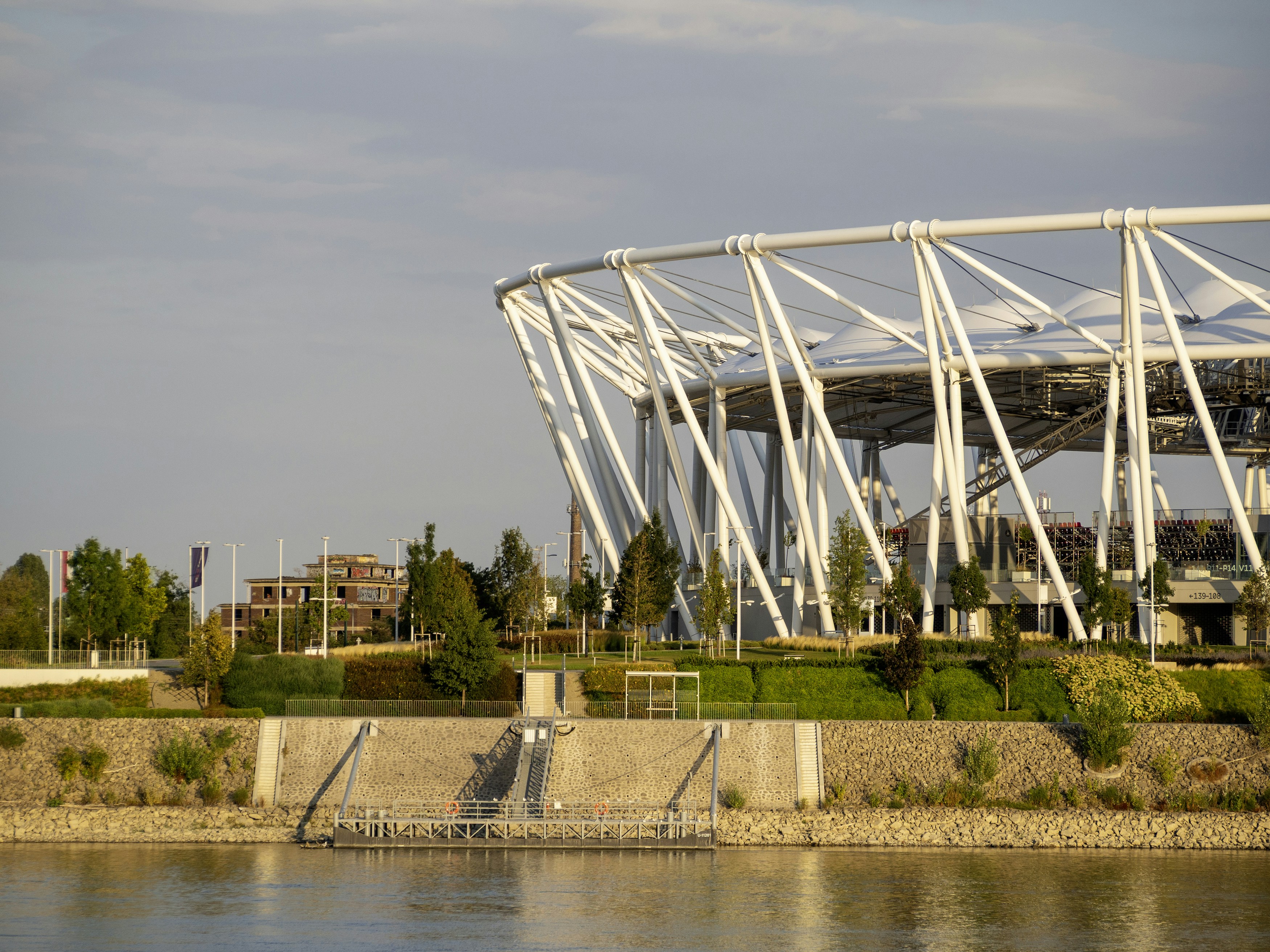 White-truss stadium rising above a riverside park