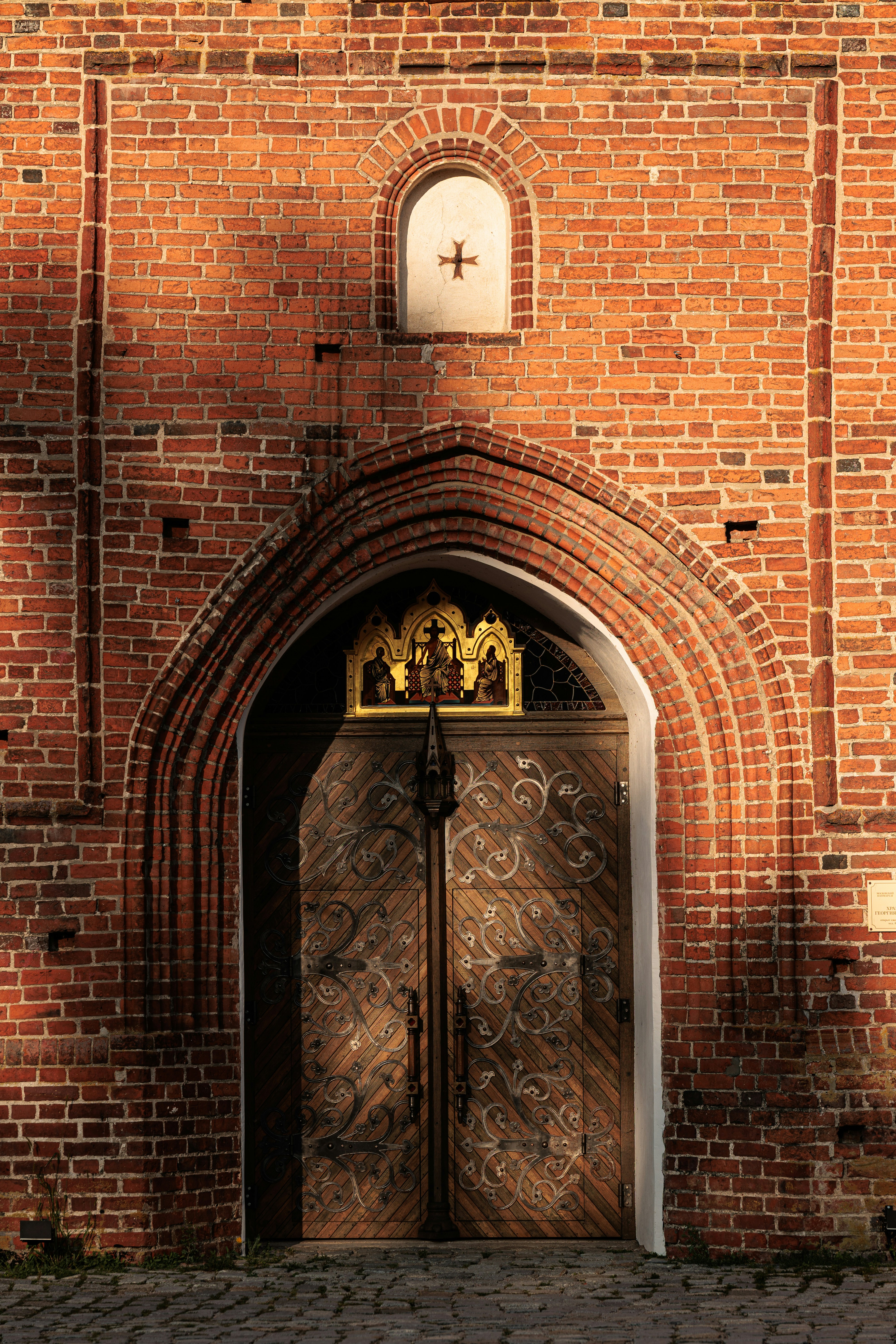 Arched Brick Portal with Ornate Iron Door under Sunlit Arch