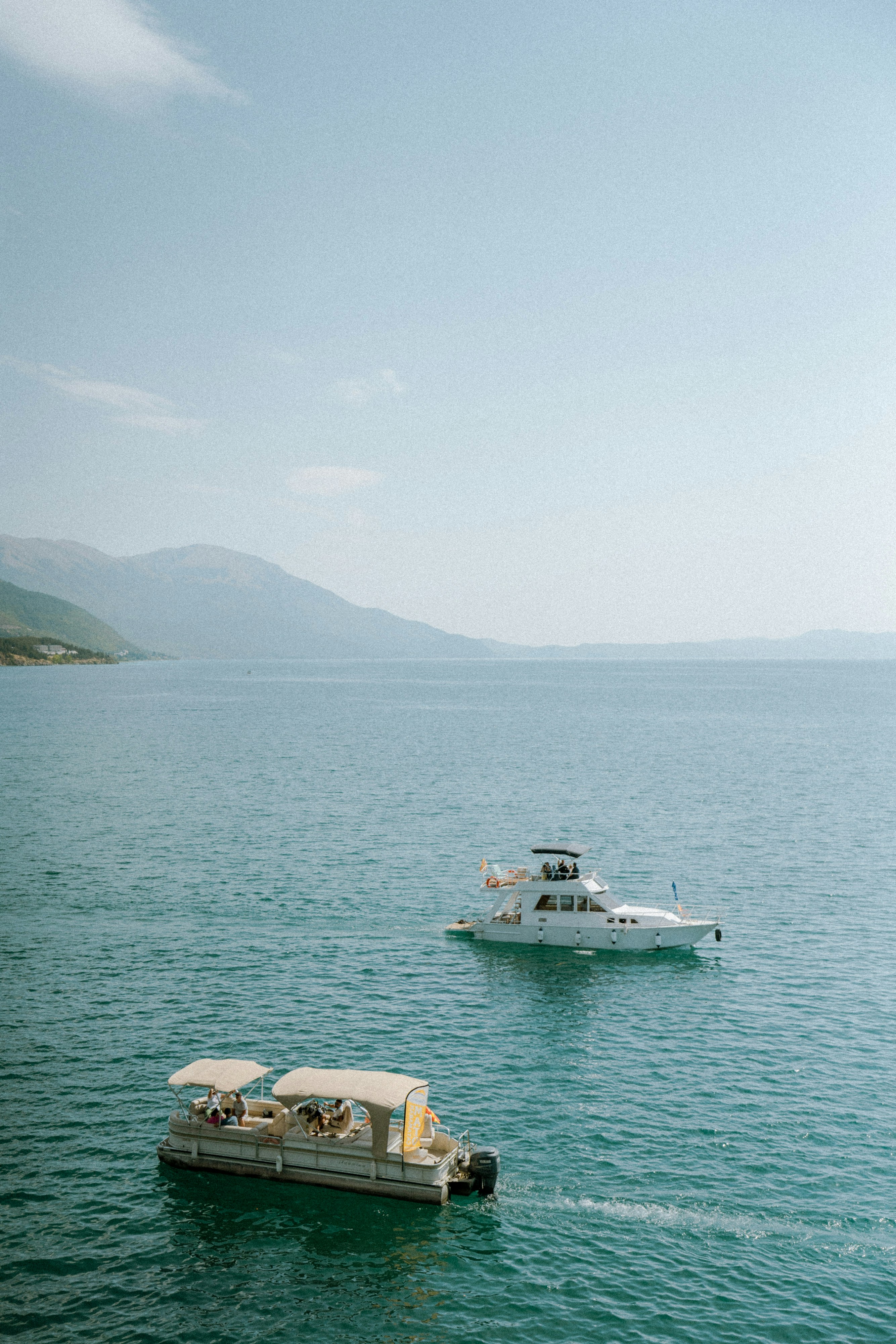 Two boats float on calm turquoise water with distant mountains under a pale blue sky.