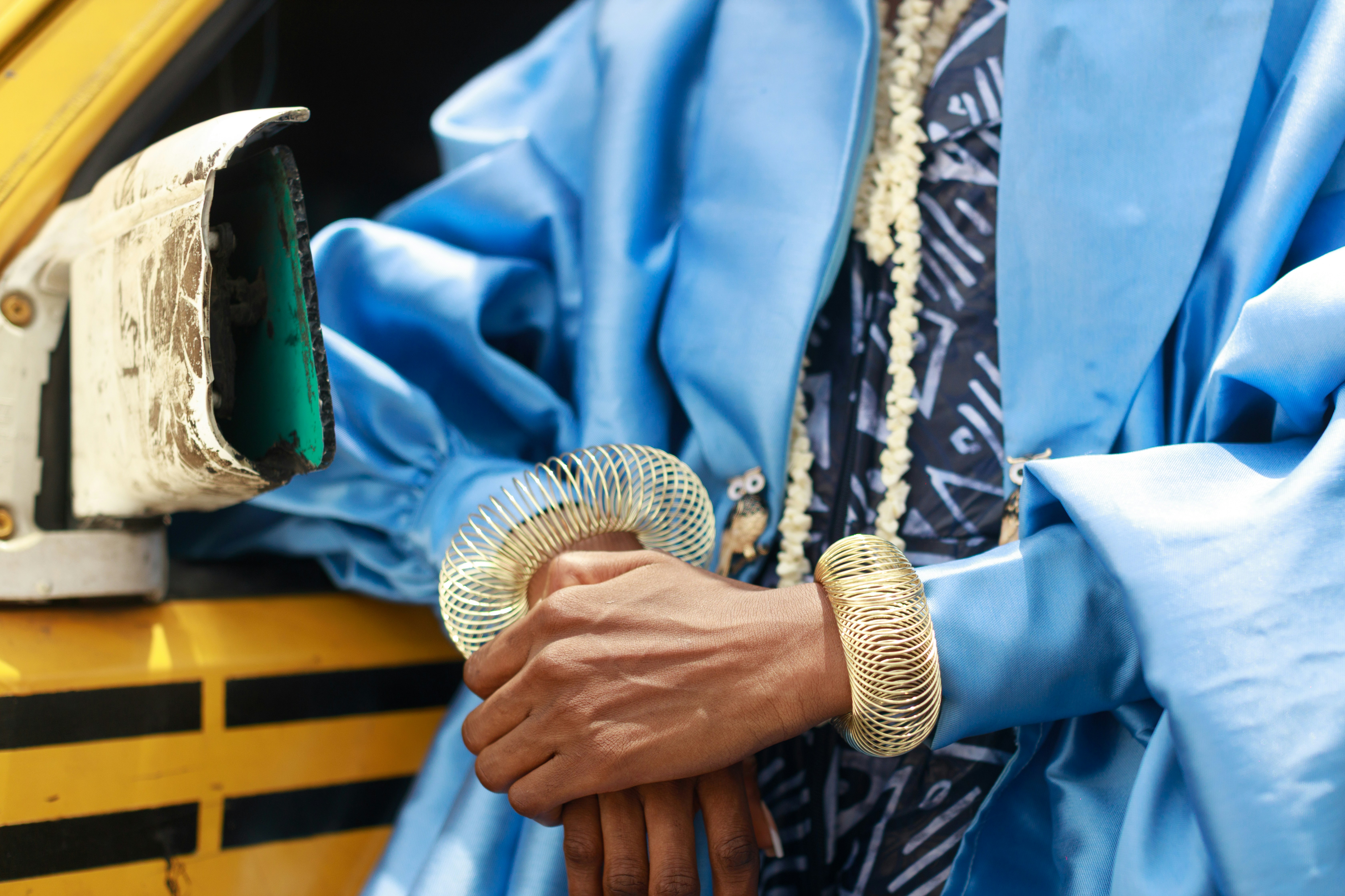 Bright Blue Cloak and Brass Bangles by a Neon Ride-Share Vehicle