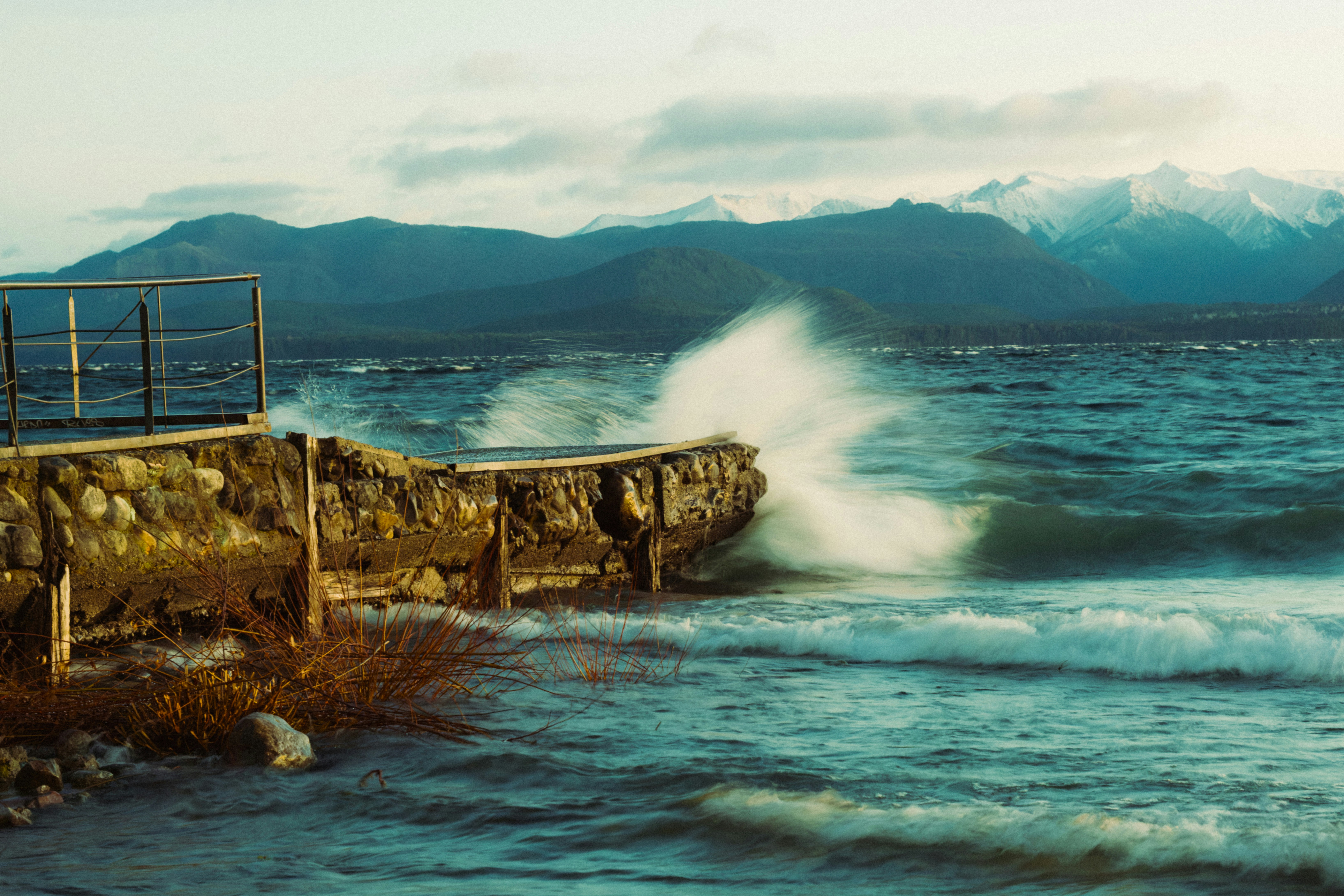 Rough Sea at the Pier: Waves Confront the Breakwater Under Mountain Shadows