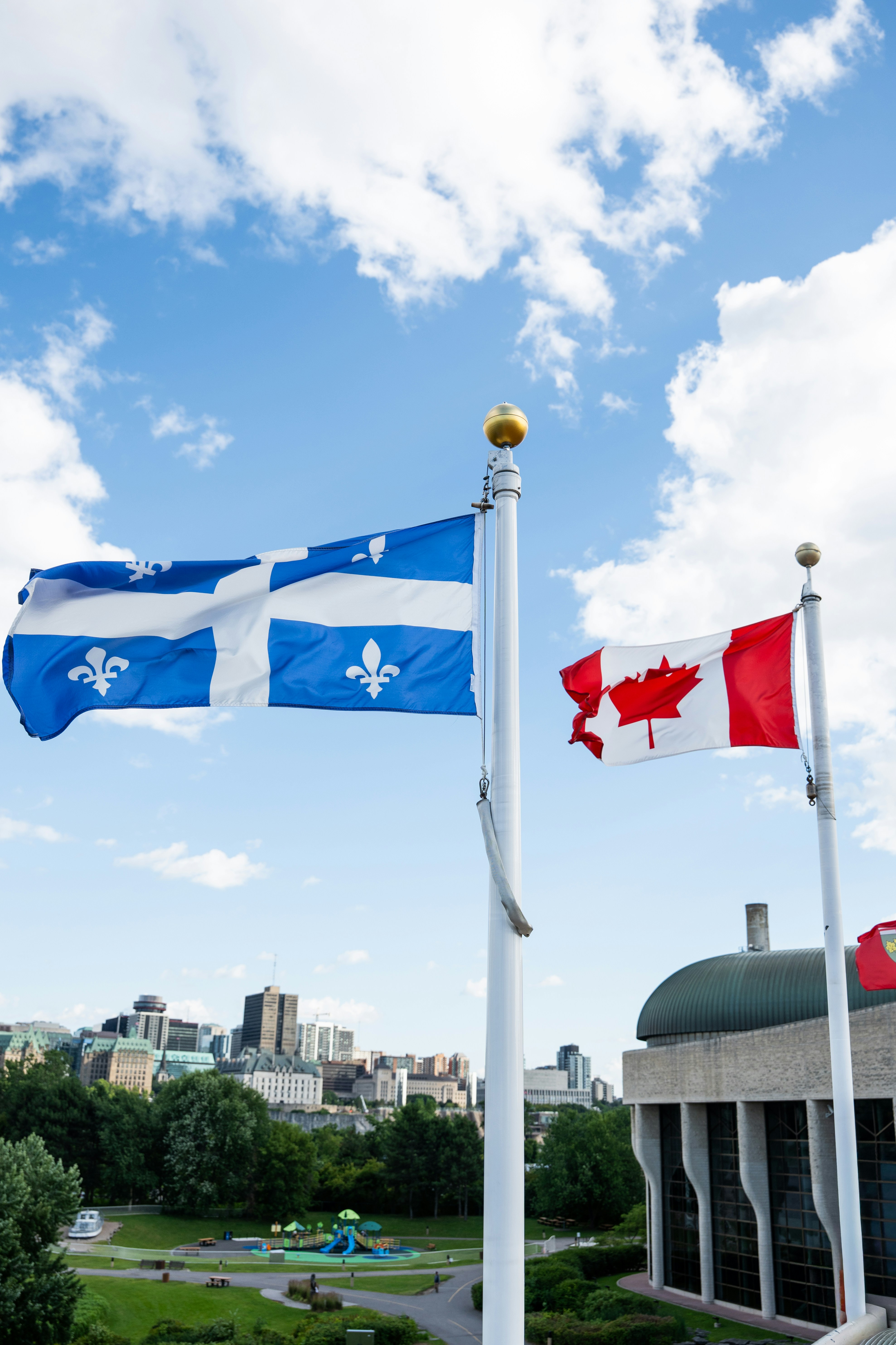 Flags Above the City: Quebec Blue and Canadian Red Flutter Over a Modern Skyline