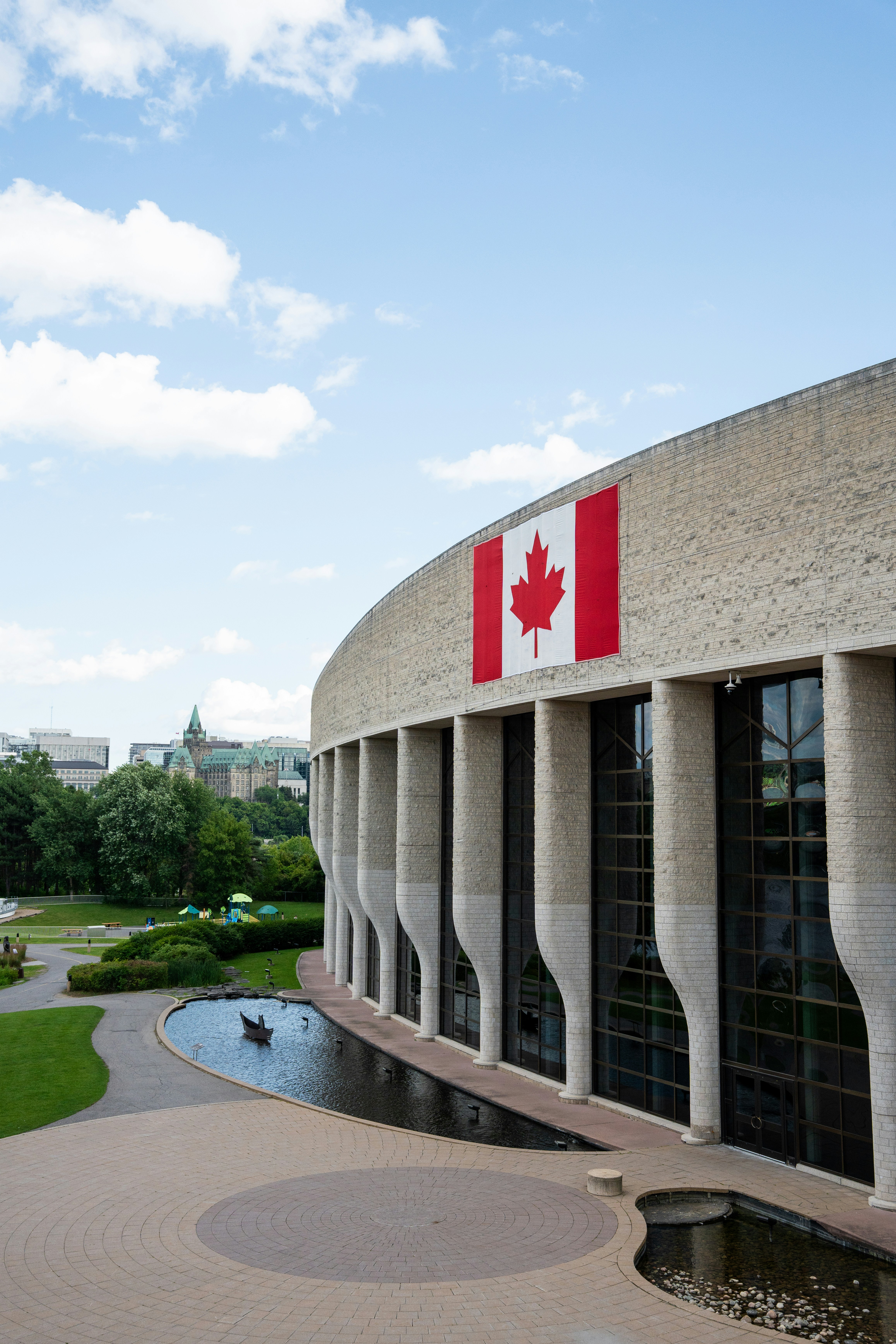 Curved civic building with a prominent Canadian flag, reflecting windows, landscaped foreground, and a tranquil water feature. This architectural scene emphasizes symmetry and national symbolism.