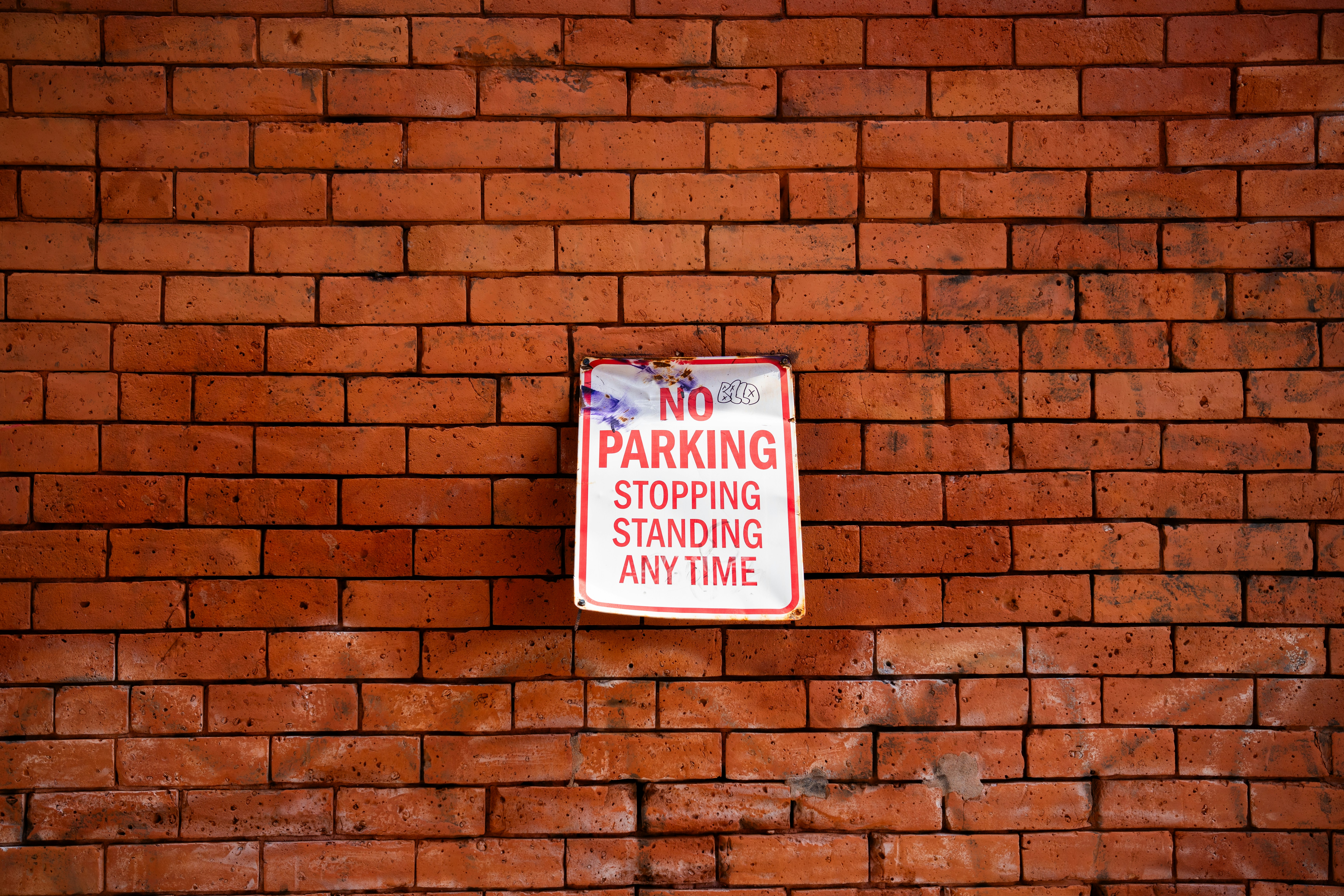 Misspelled No Parking sign anchored to weathered brick facade