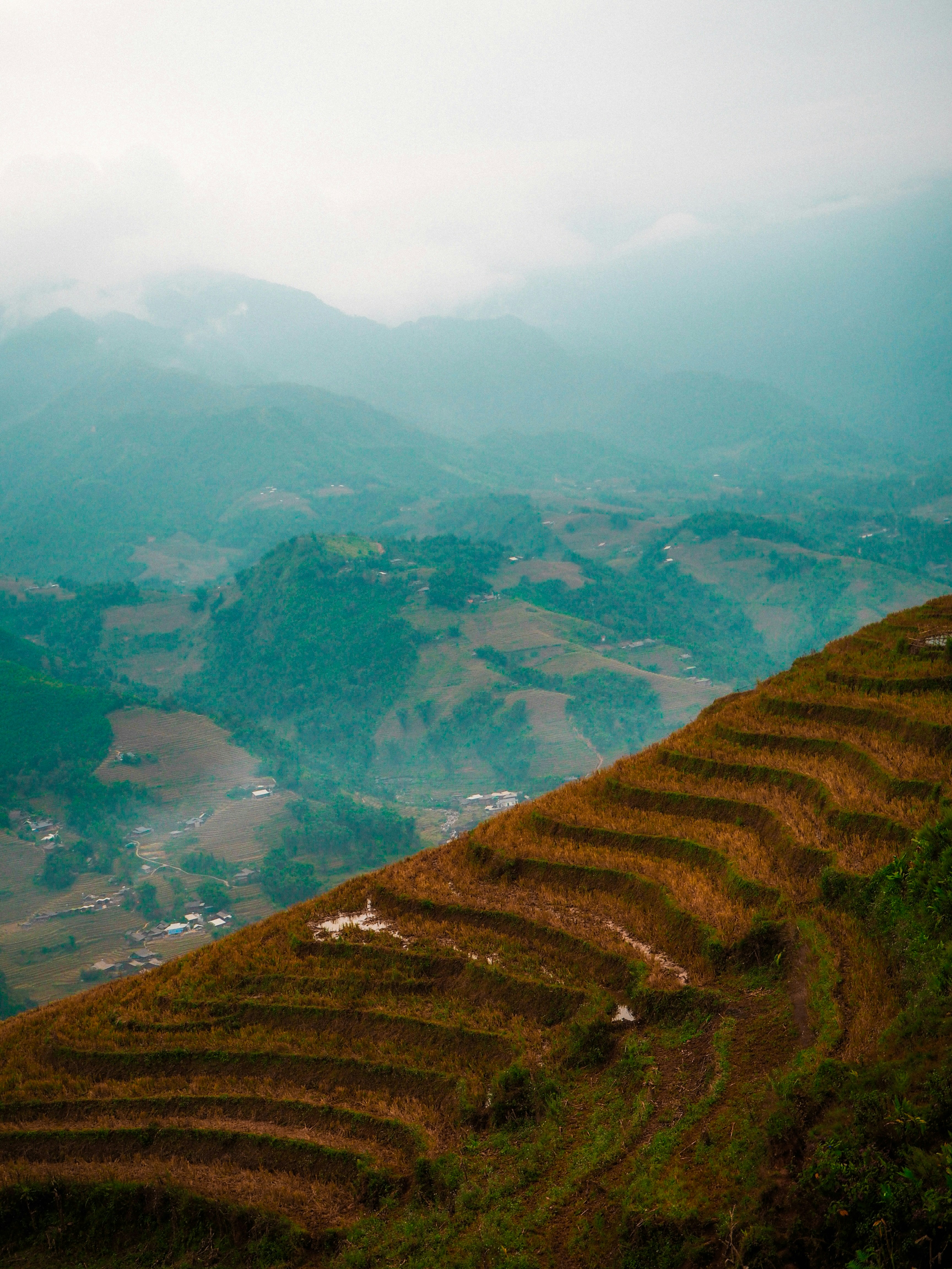 Terraced hillside folds into a misty valley with distant villages and rolling green fields.