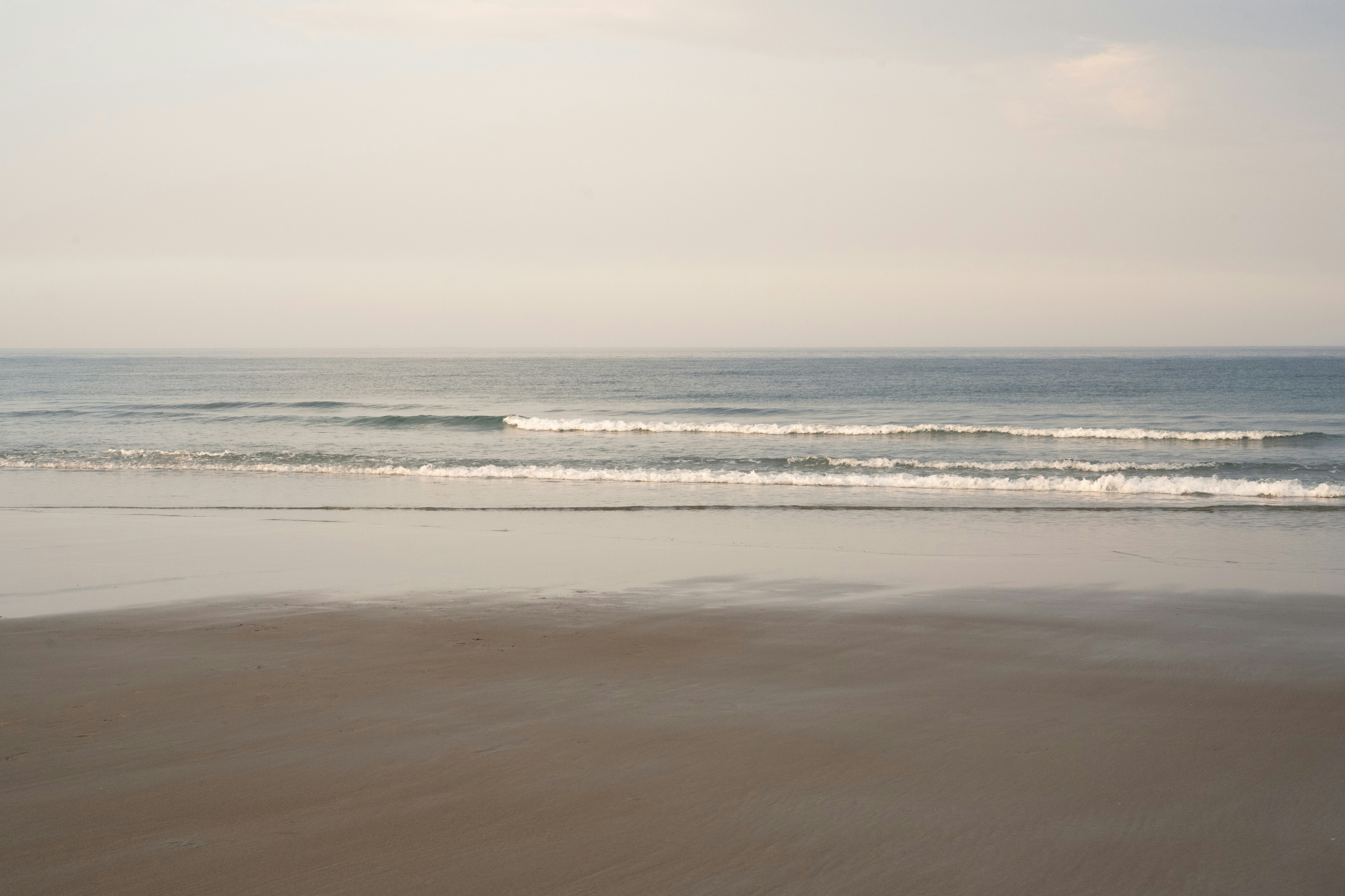 Soft seaside scene with a calm horizon and gentle waves; a minimalist coastal landscape captured with muted tones. This is a photographic still rather than a logo, illustration, painting, or cartoon.