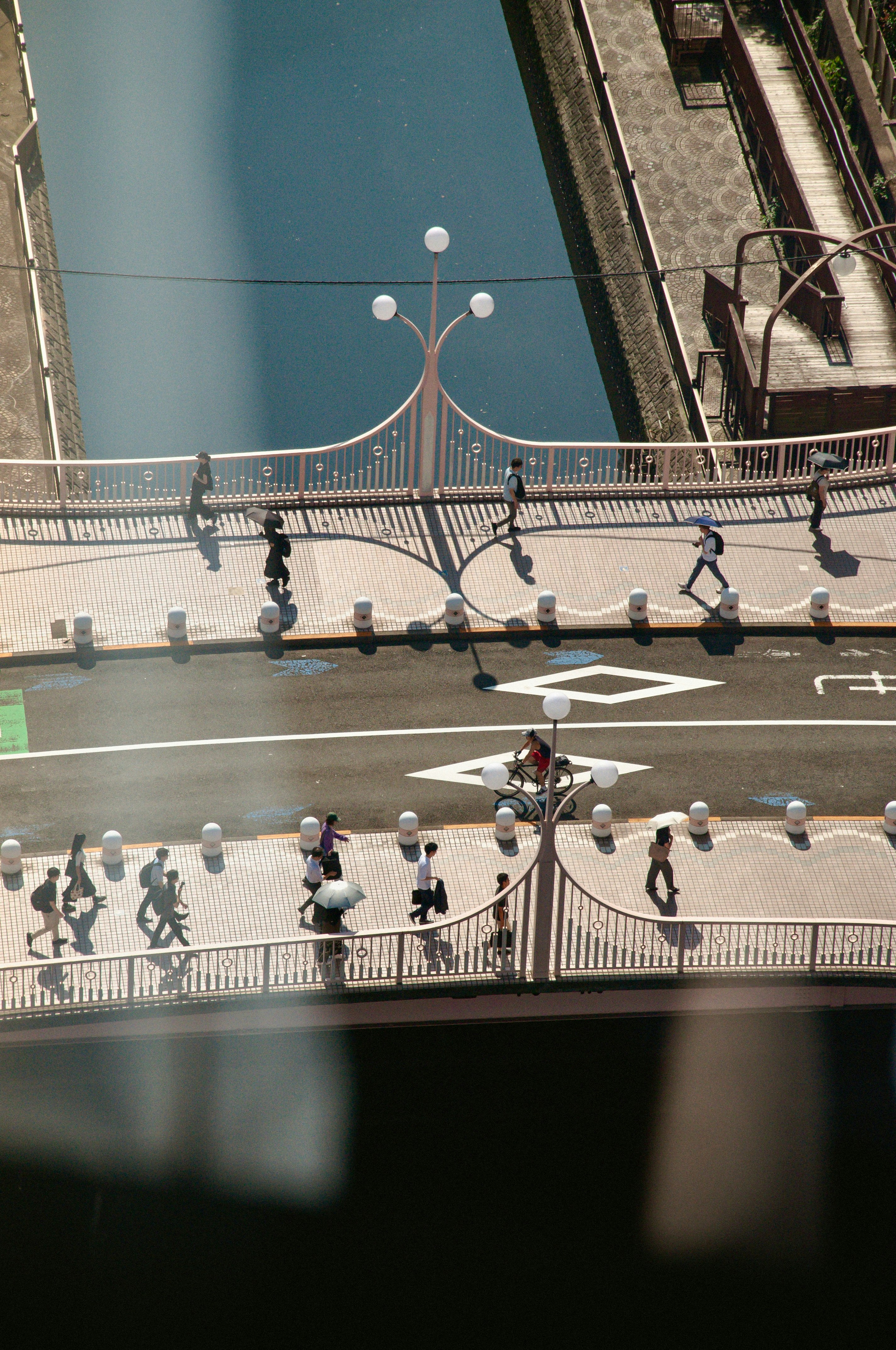 Bridge silhouettes and pedestrians cast in midday light above a waterway