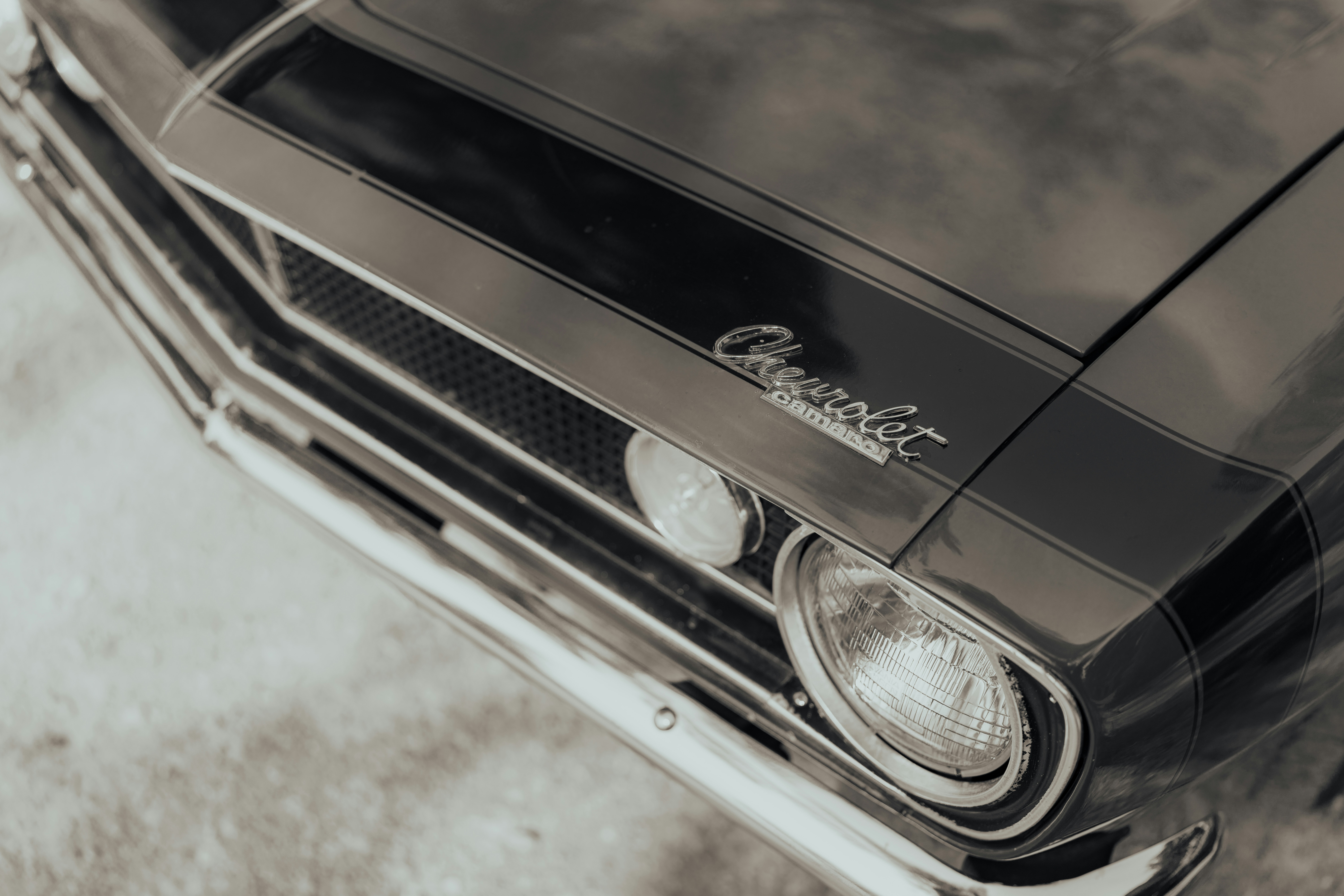 Close-up of a vintage car hood with the Chevrolet emblem and round headlight, emphasizing chrome details and smooth reflections.