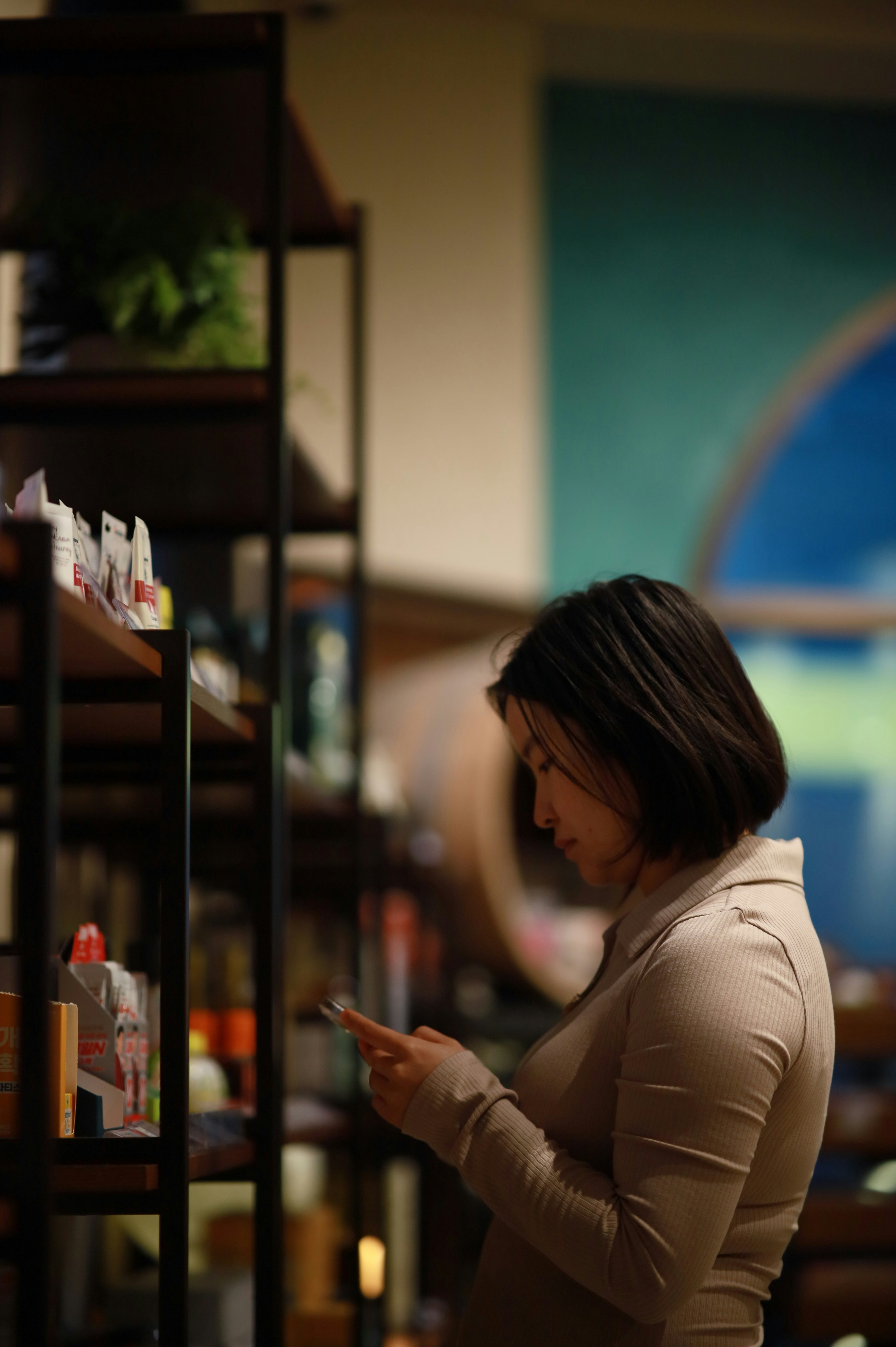 A woman in a beige shirt looking at her phone in a shop